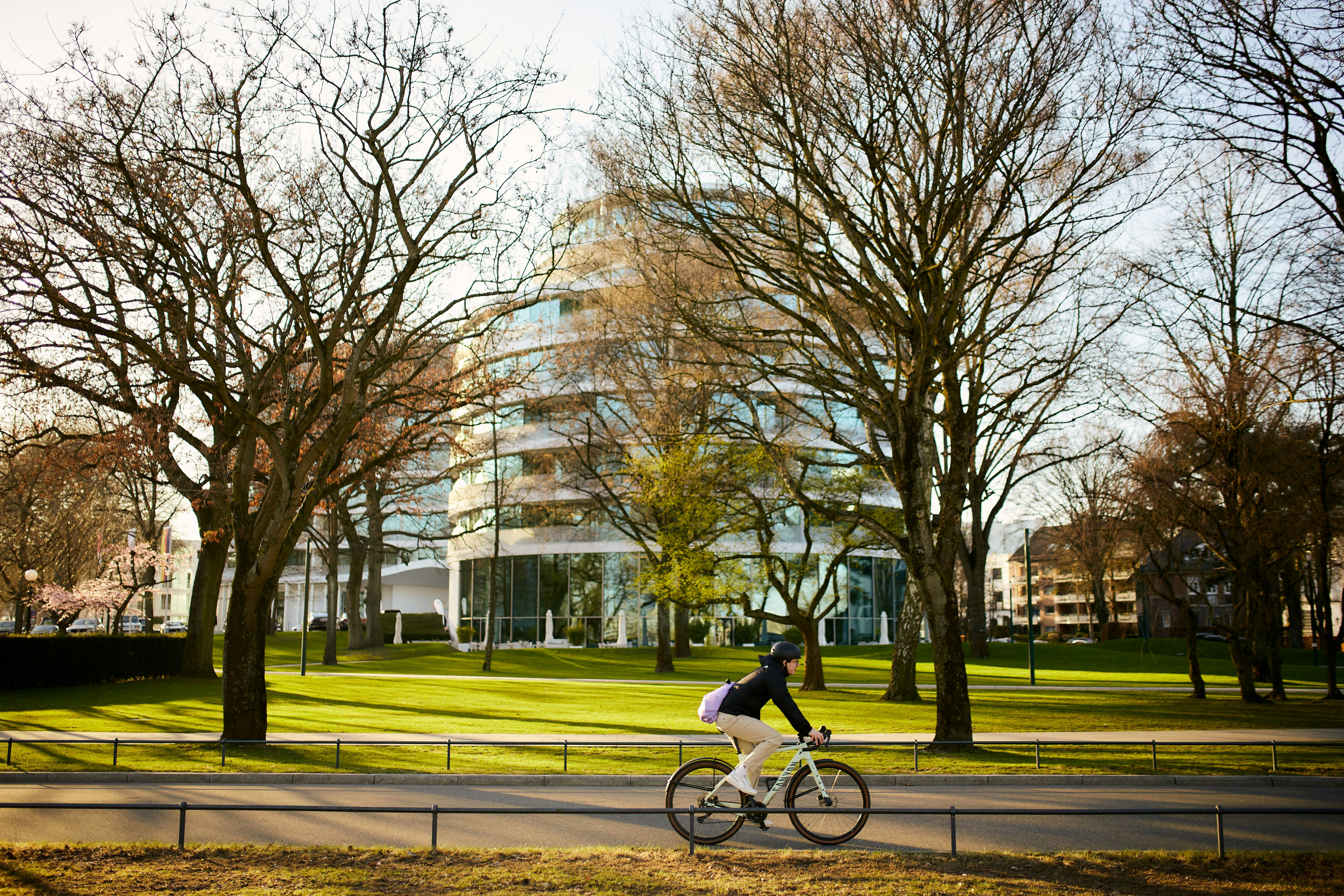 Rider in a sunlit urban park trails a modern glass-clad campusOleksandr Parfeniuk