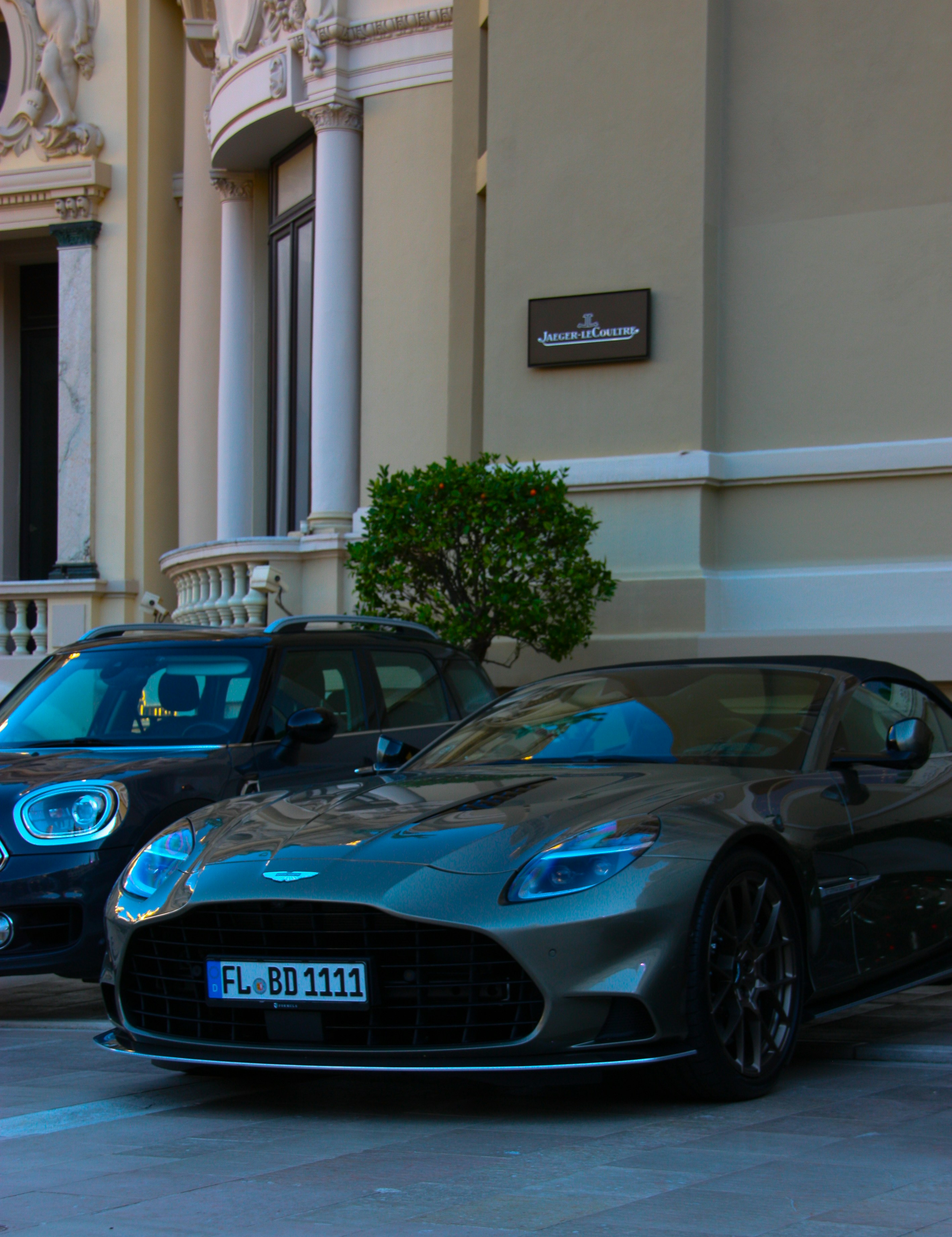 Two luxury cars parked in front of an ornate building with a plaque, highlighting the glossy reflections and architectural backdrop.
