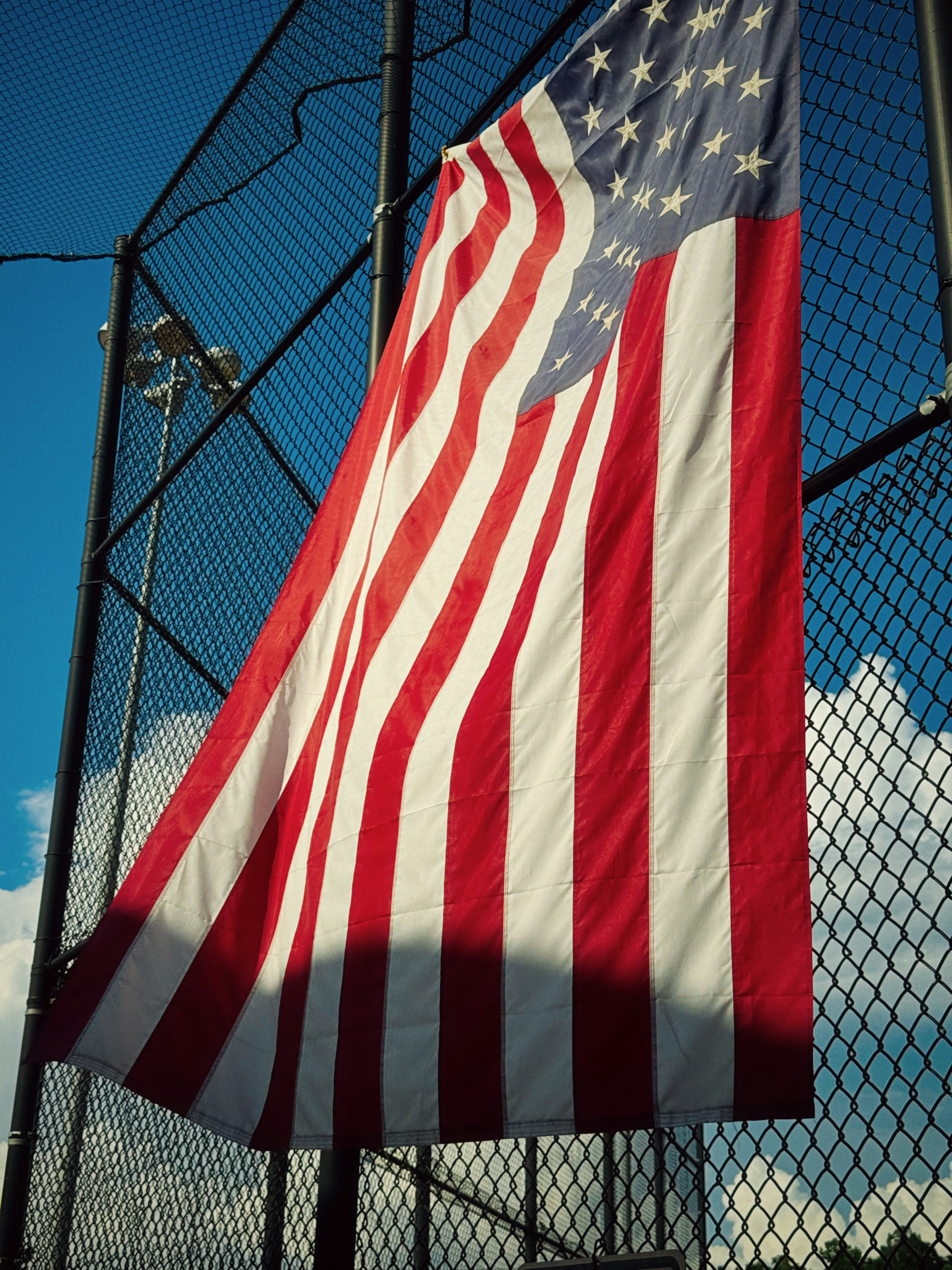 Flag on the Fence: Bold Stripes Against Chain-Link Sky