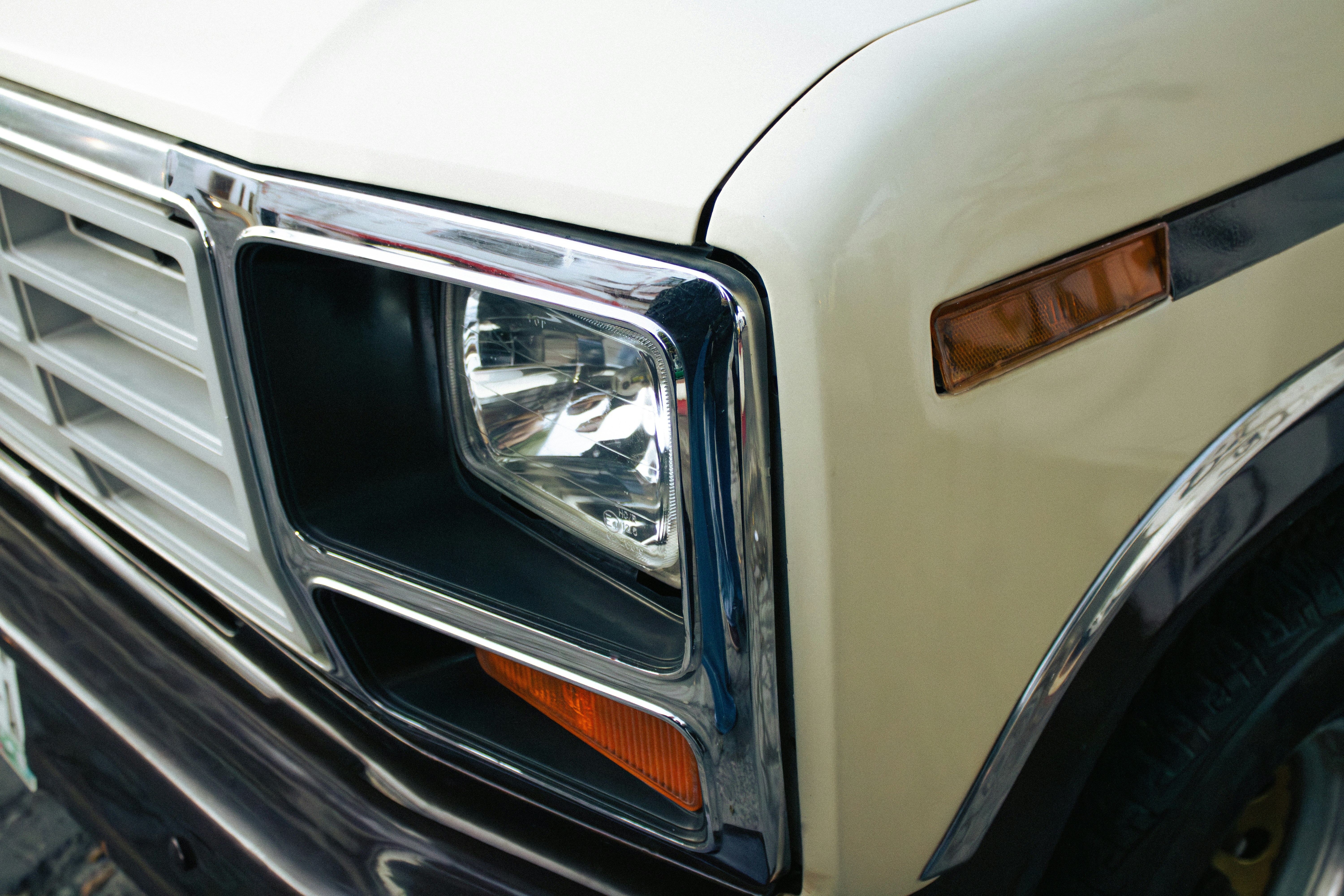 Close-up of a vintage beige pickup’s headlamp and chrome grille
