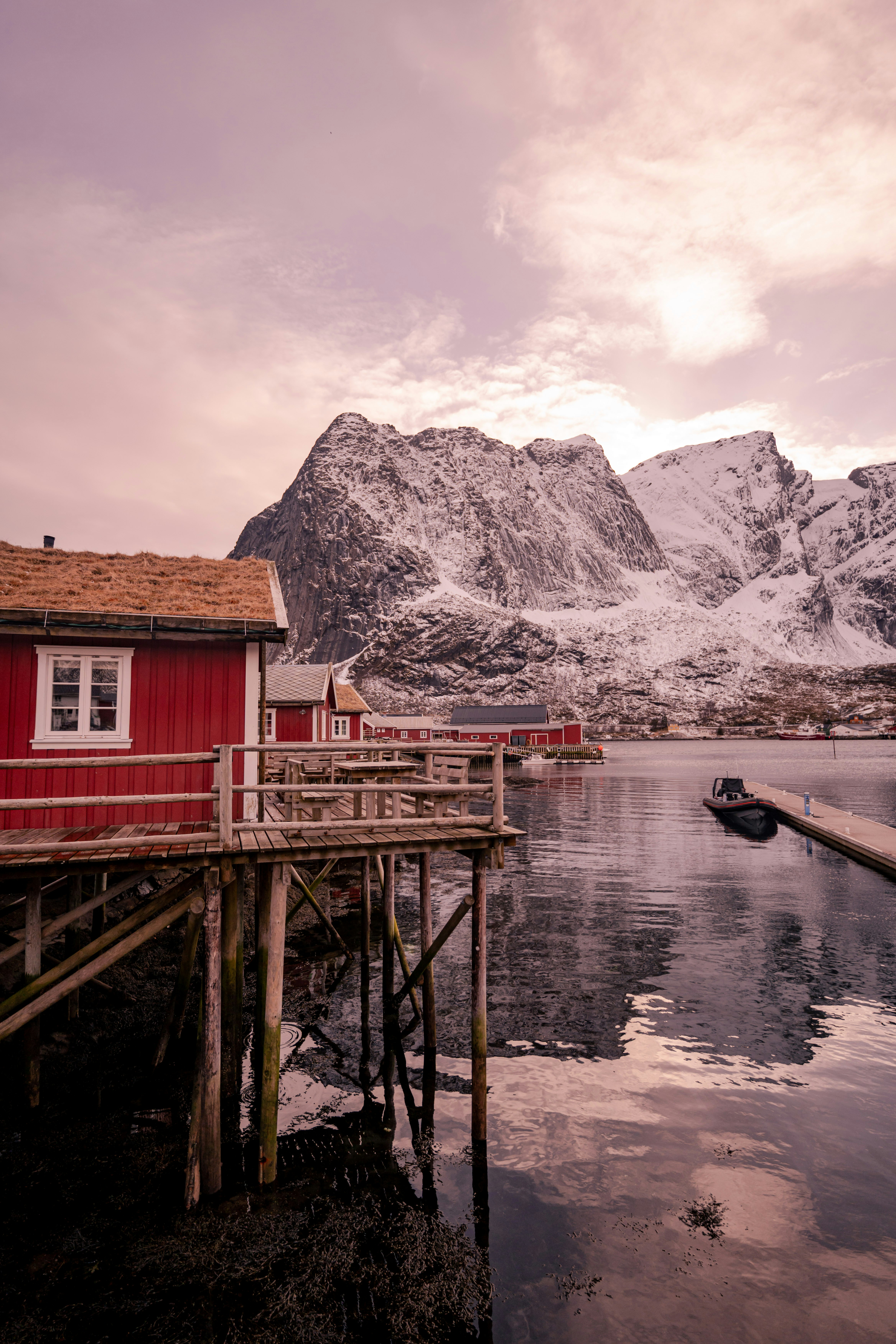 Red cabins on stilts by a calm fjord with snow-capped peaks