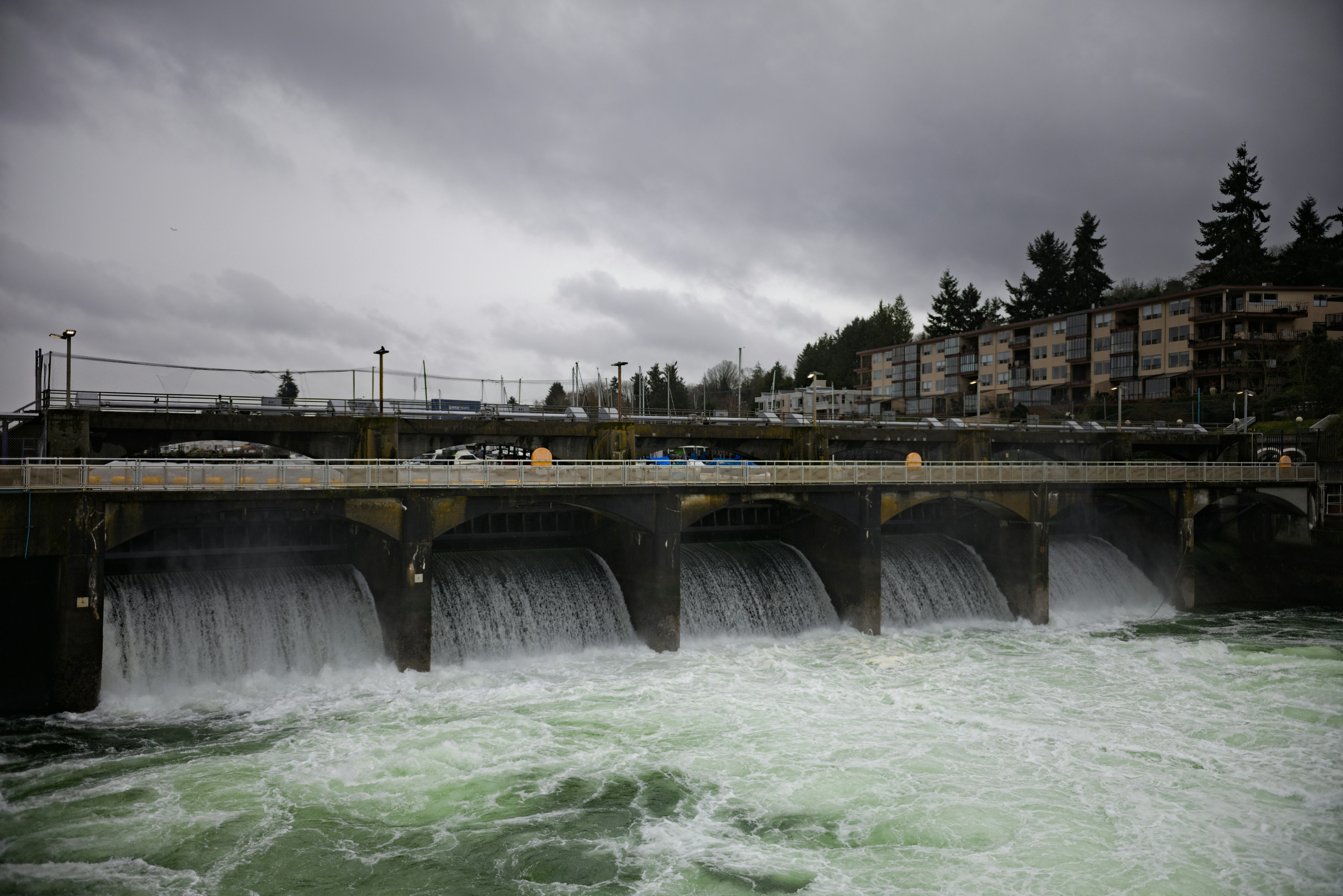 Overcast Cascade: Water frees over a river dam beneath a quiet bridge