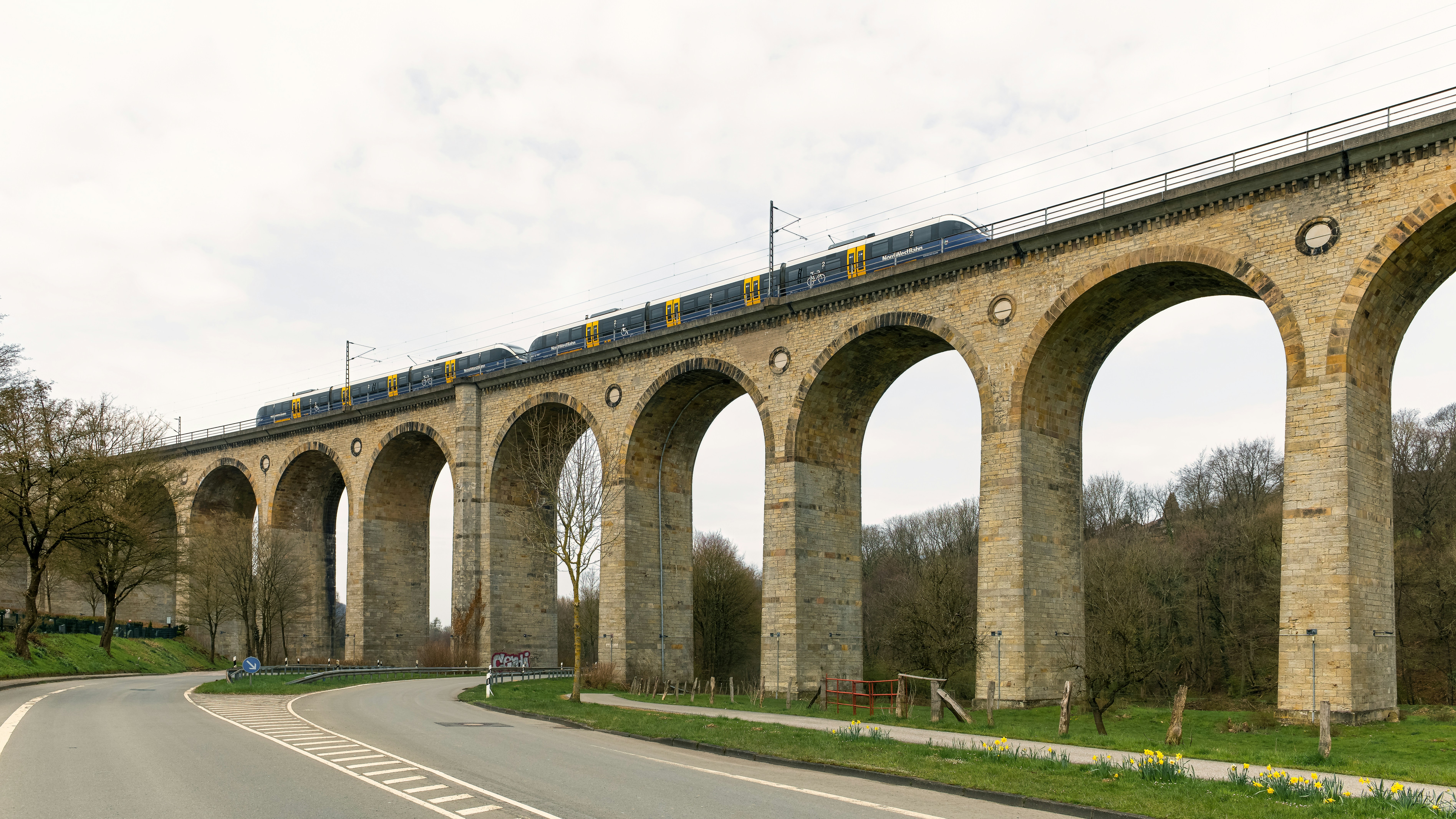 Viaduct in Motion: Trains crossing a stone archway above a winding road
