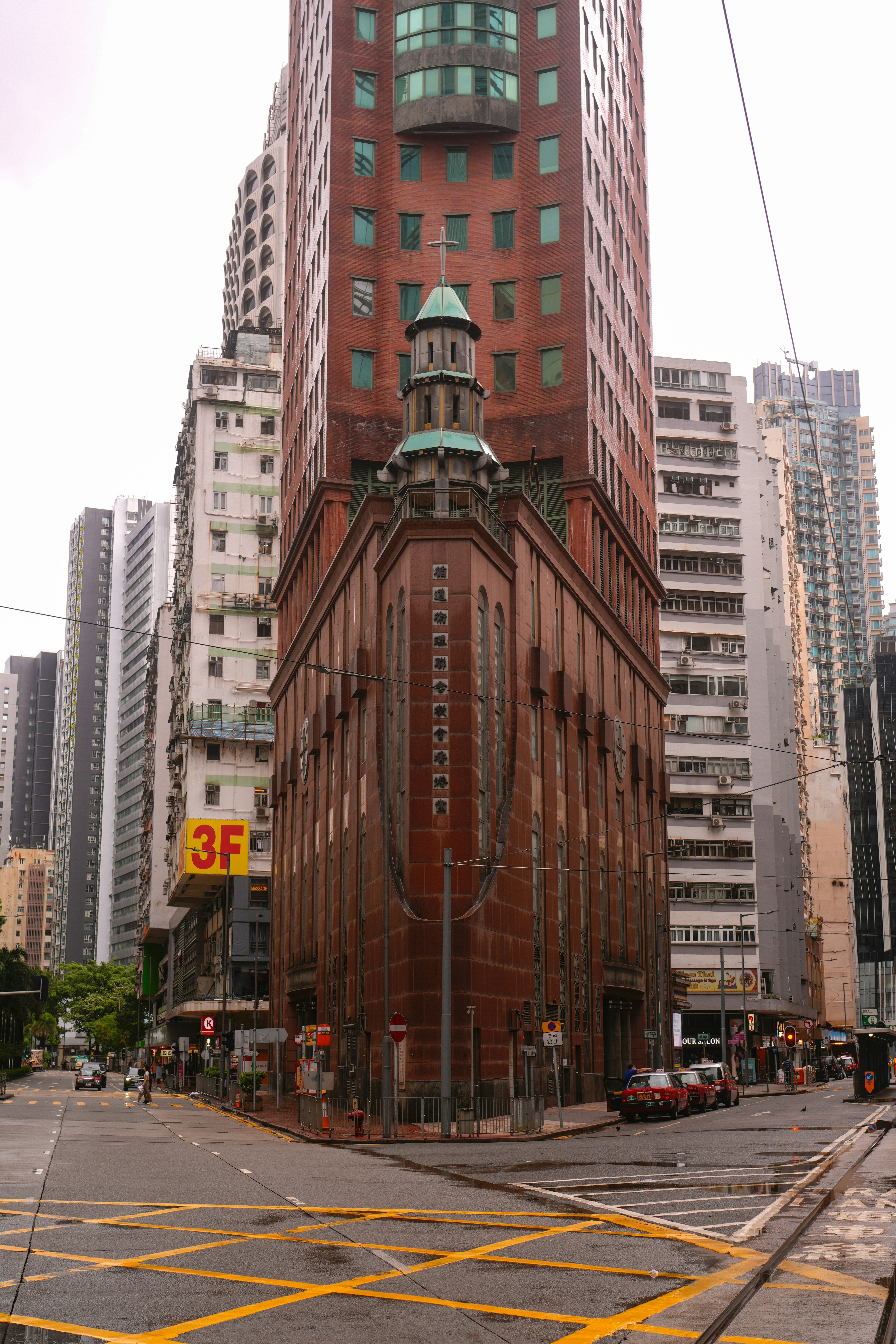 Tall brick building with a church spire in a city.
