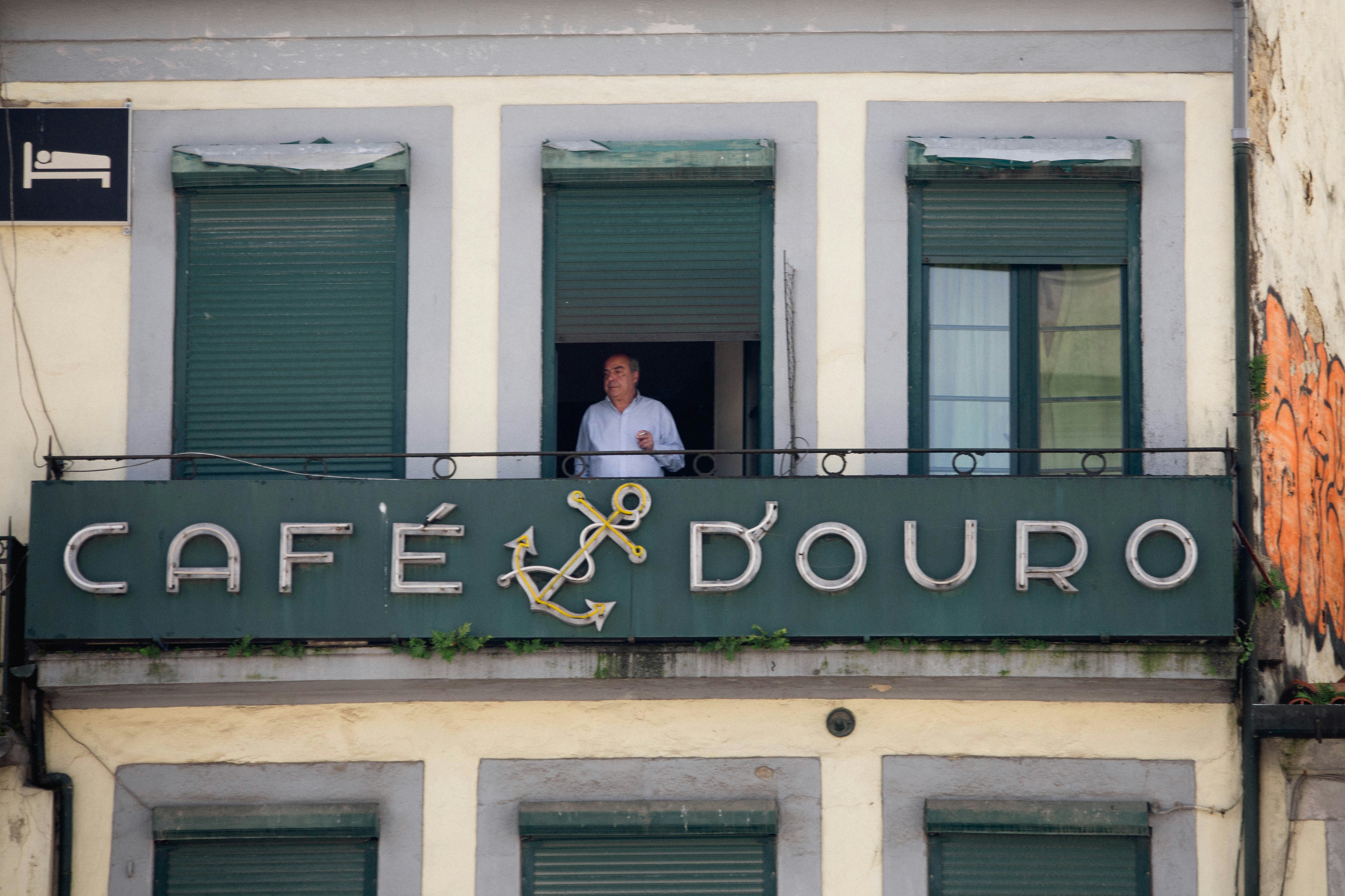 Window to the Café: A Man on the Balcony Above the Green Sign