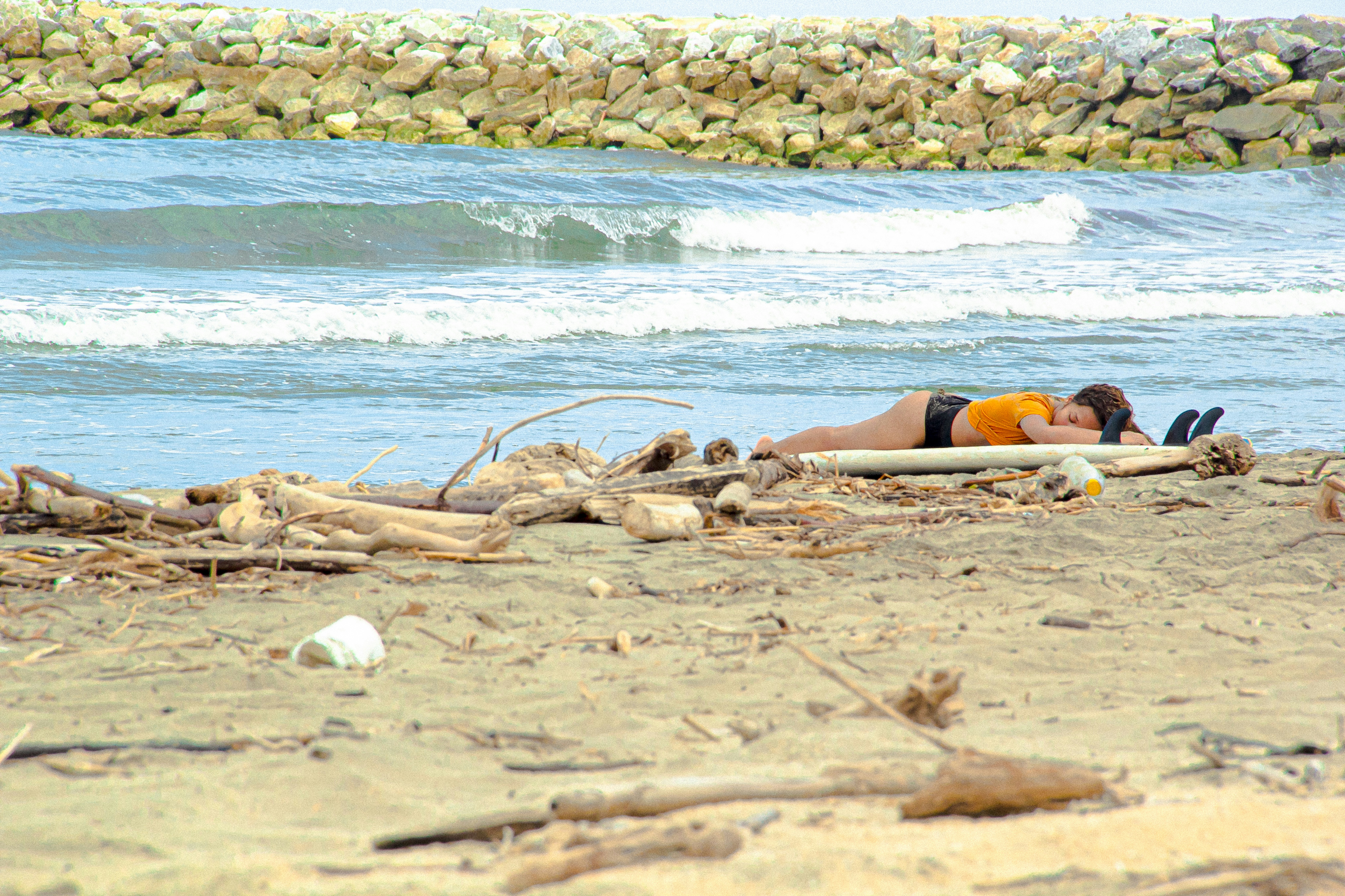 Sunlit Rest: A lone figure snoozes on a driftwood-strewn beach