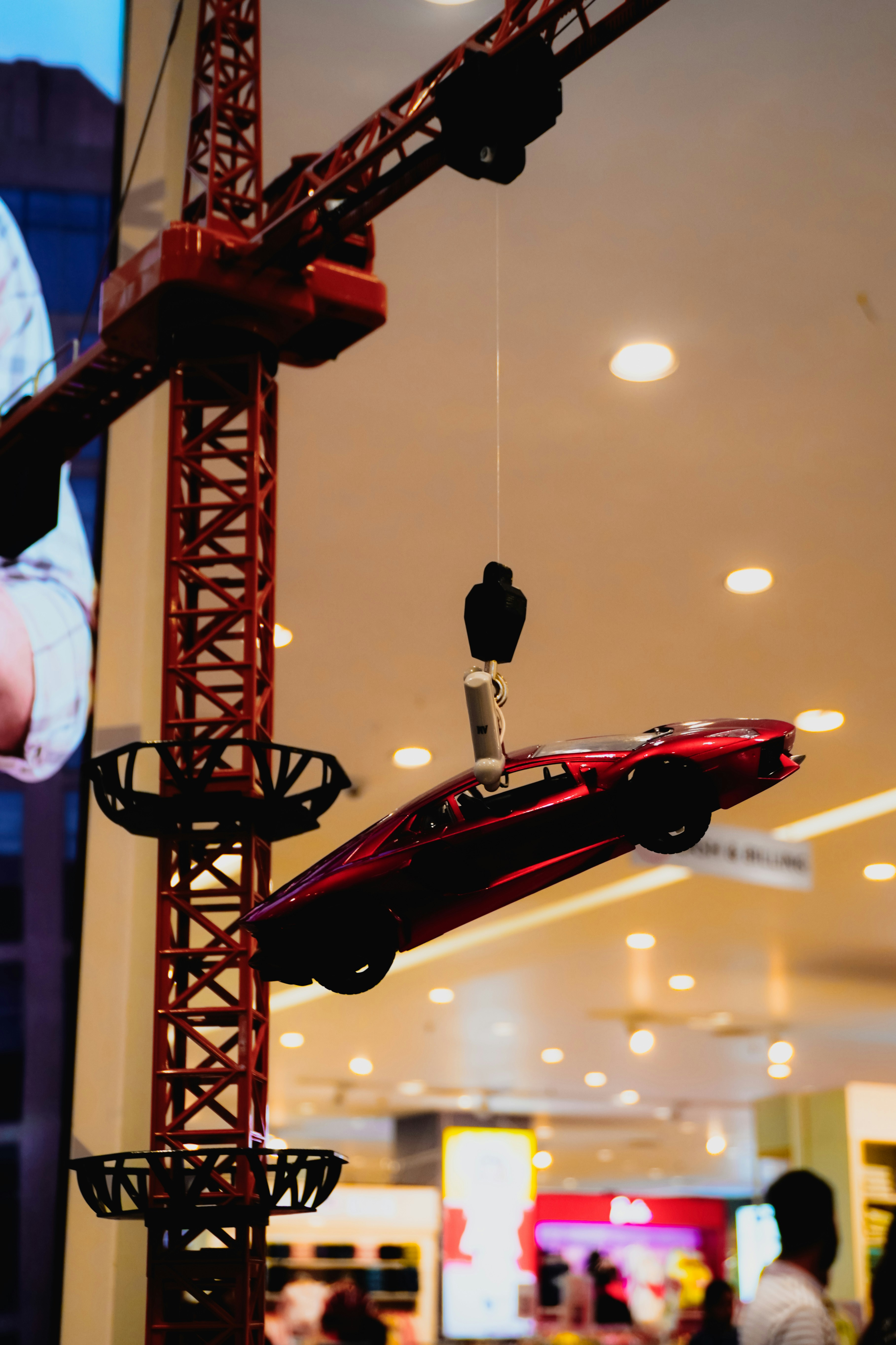 Miniature red sports car suspended over a crane in a bustling indoor display