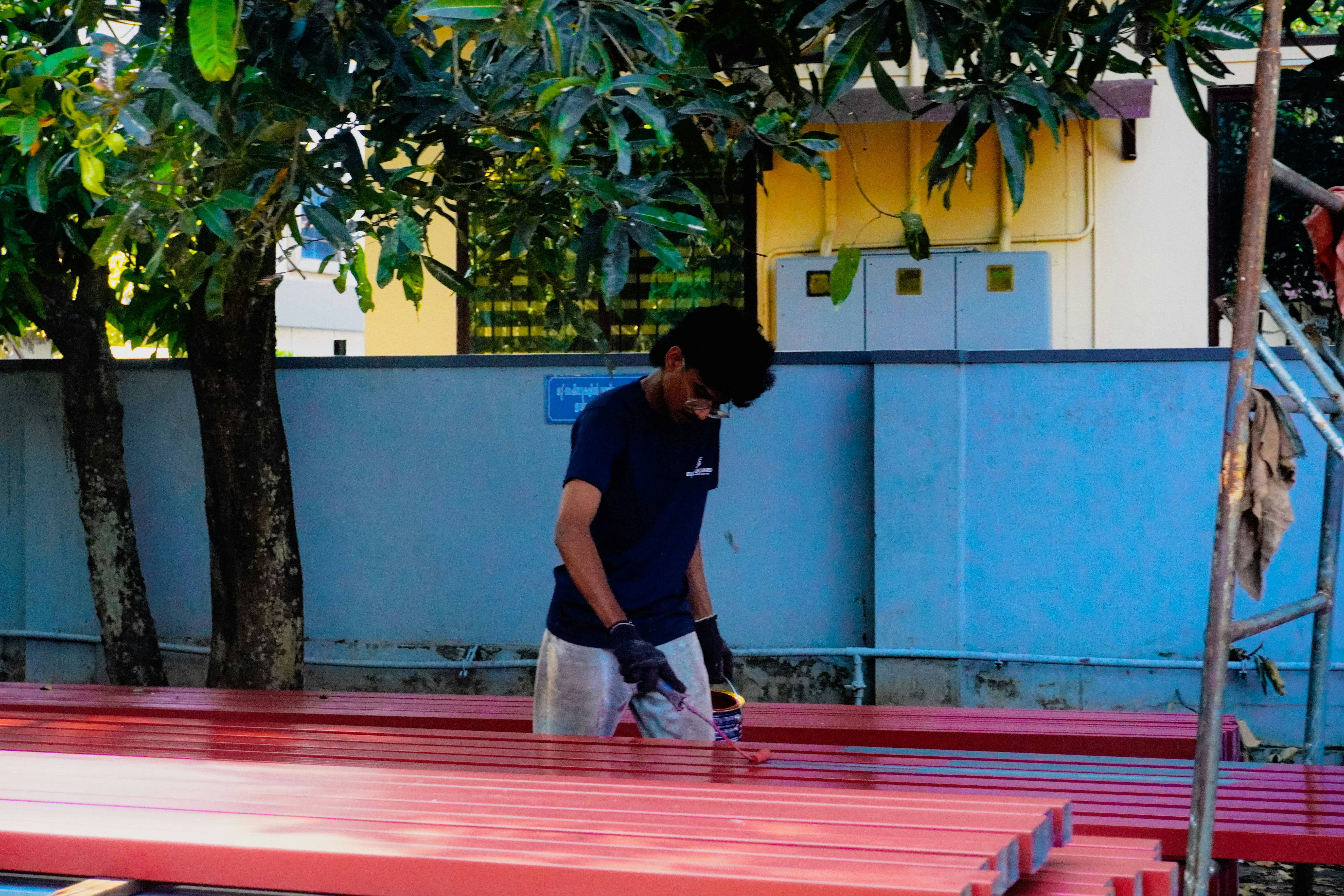 Worker at a metal roofing yard beneath a leafy canopy