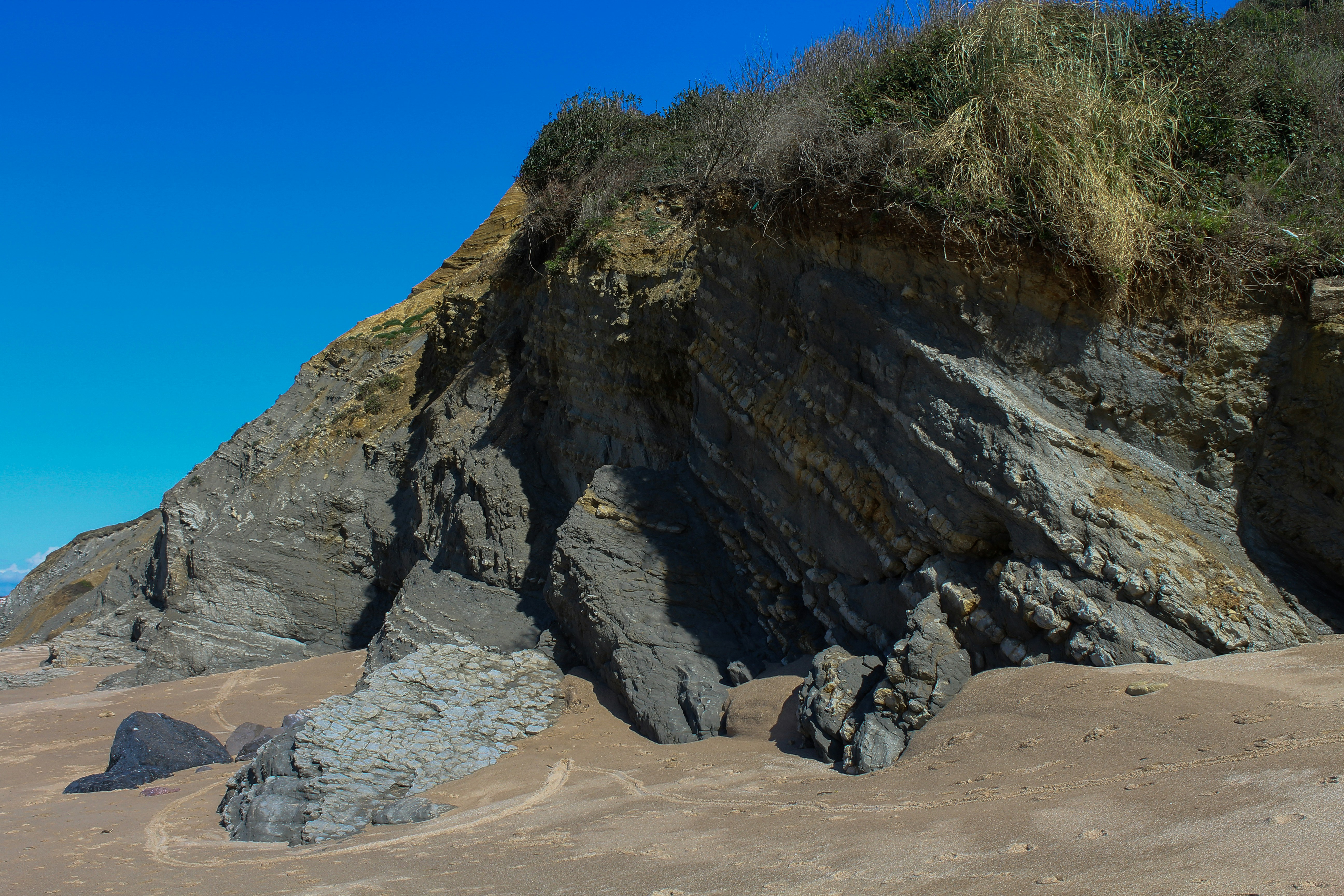 Geologic Cliffs at Low Tide: Rugged Rock Formations Meeting Sandy Shore