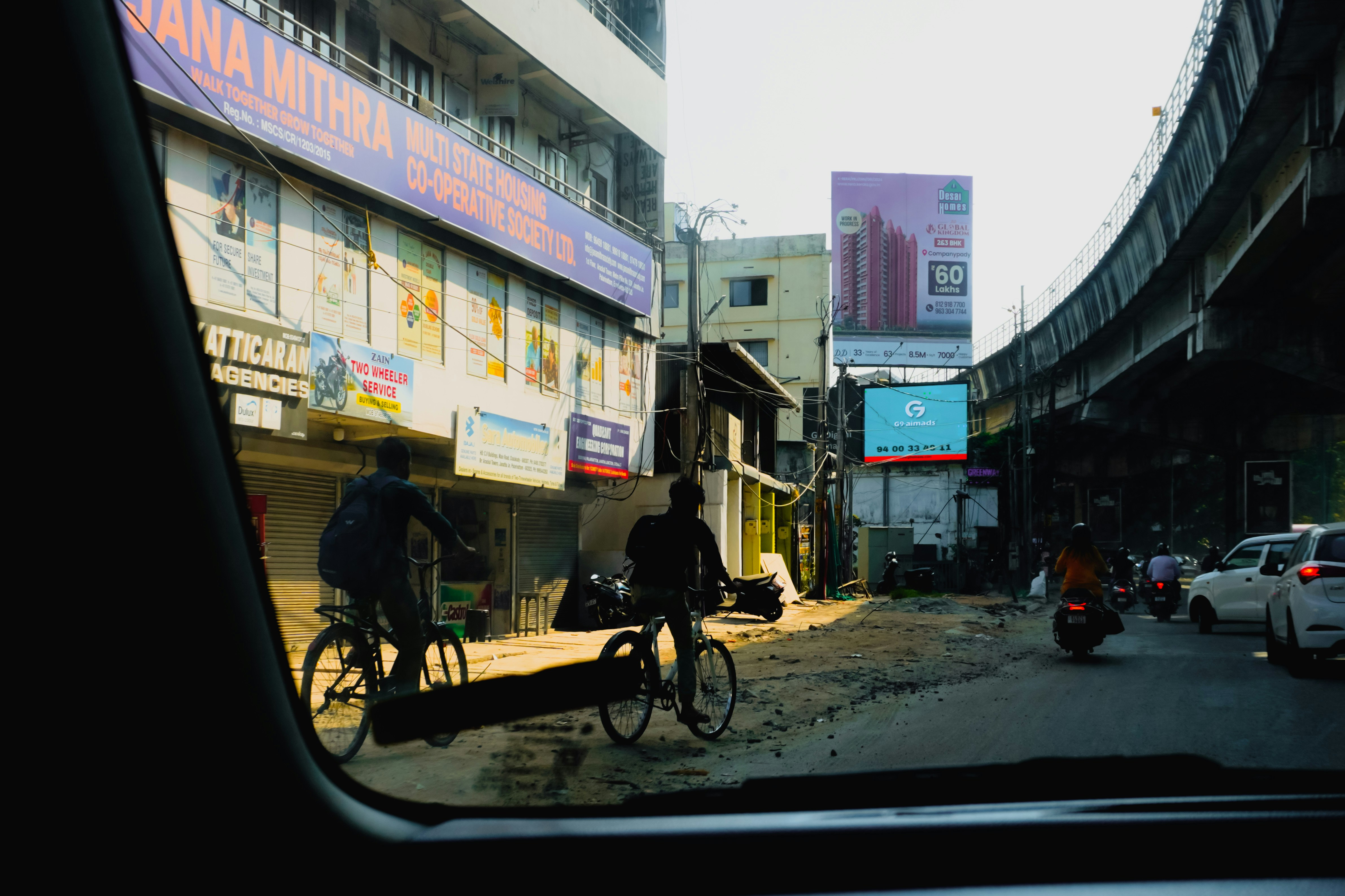 Streetfront Vigil: Cyclists and Shops Framing a Busy Corridor