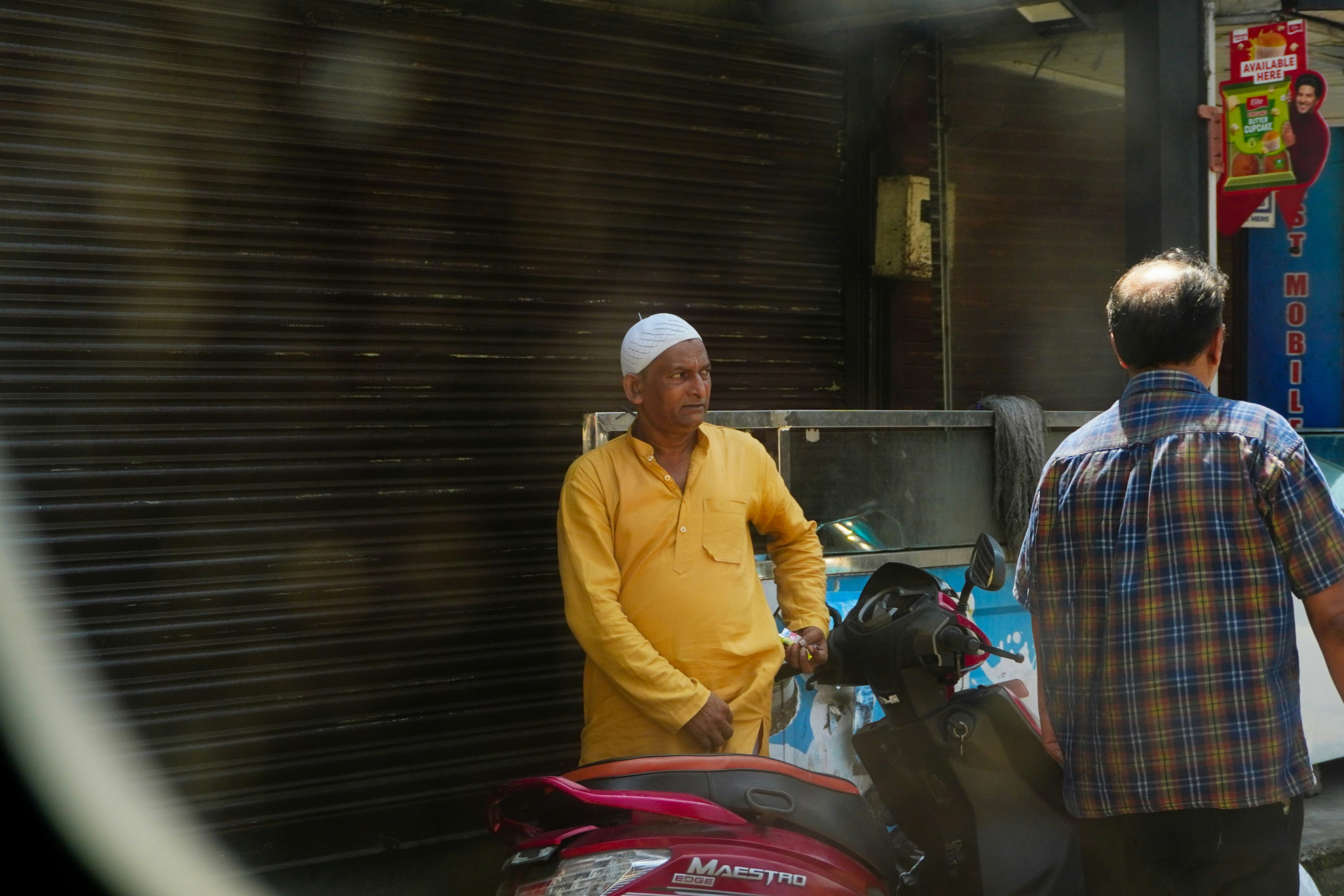 Yellow-shirted vendor by a parked scooter under shop shutters