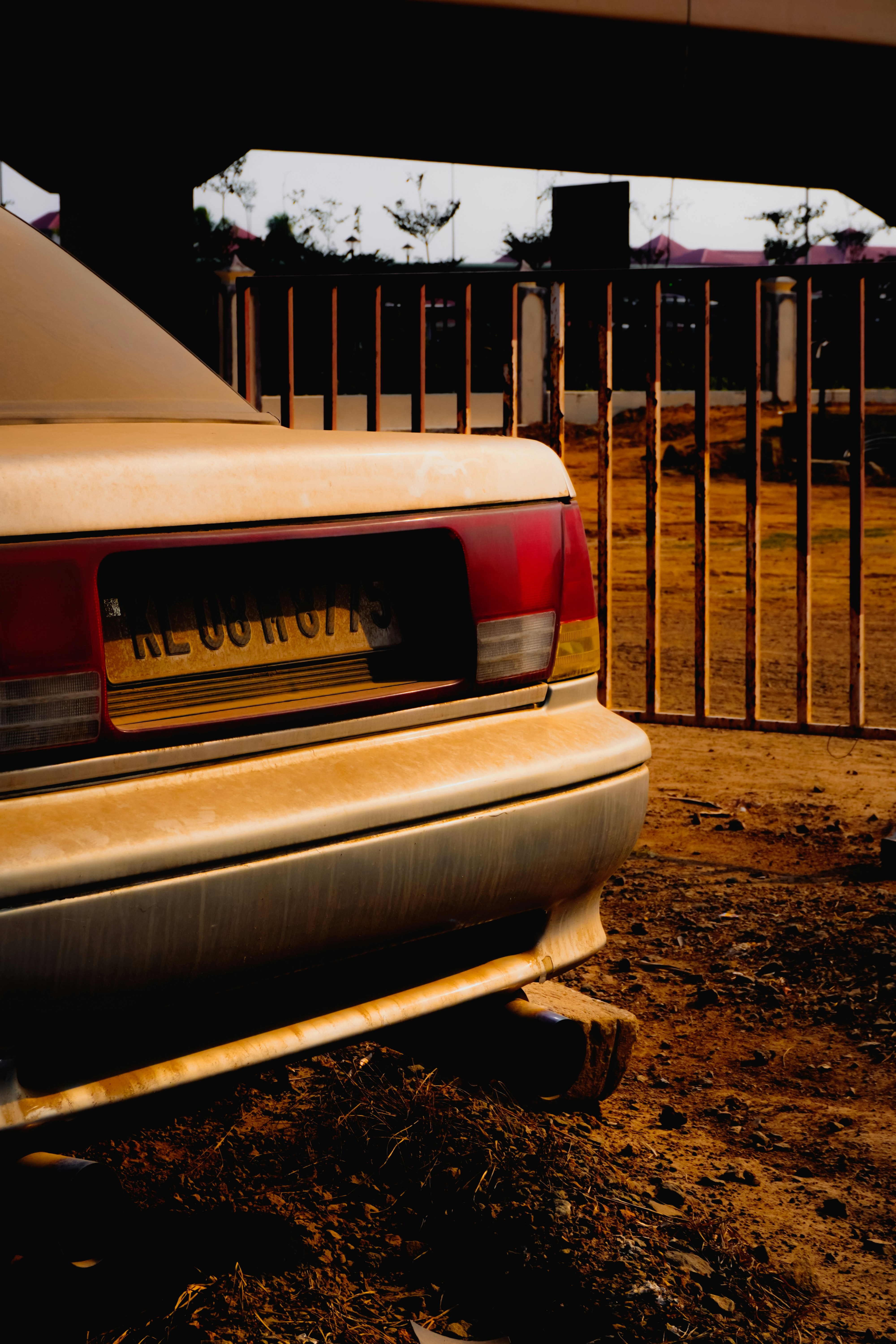 Dusty rear of a parked sedan under a shelter at sunset