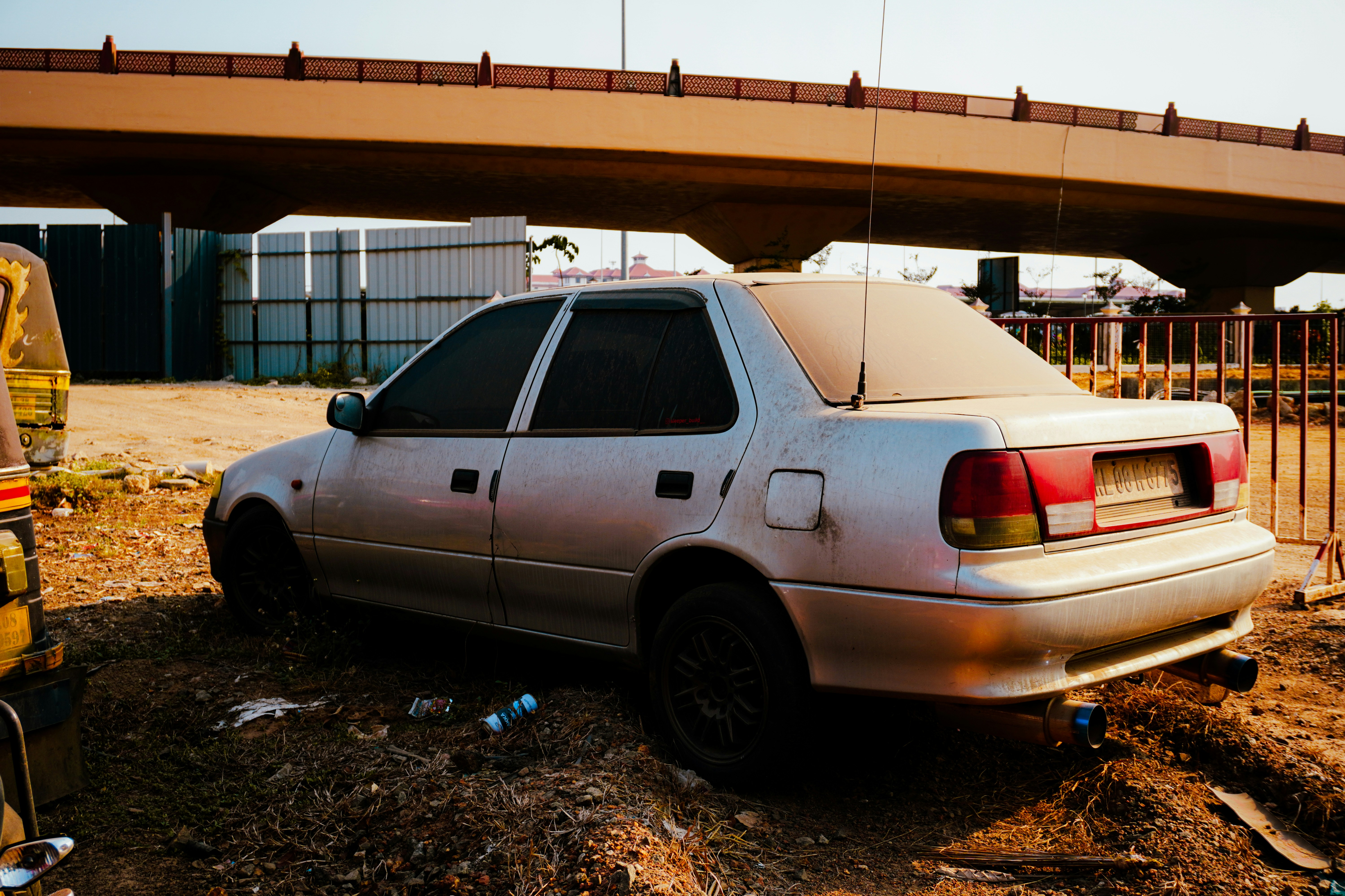 Dusty sedan under the overpass: a quiet relic in a sunlit lot