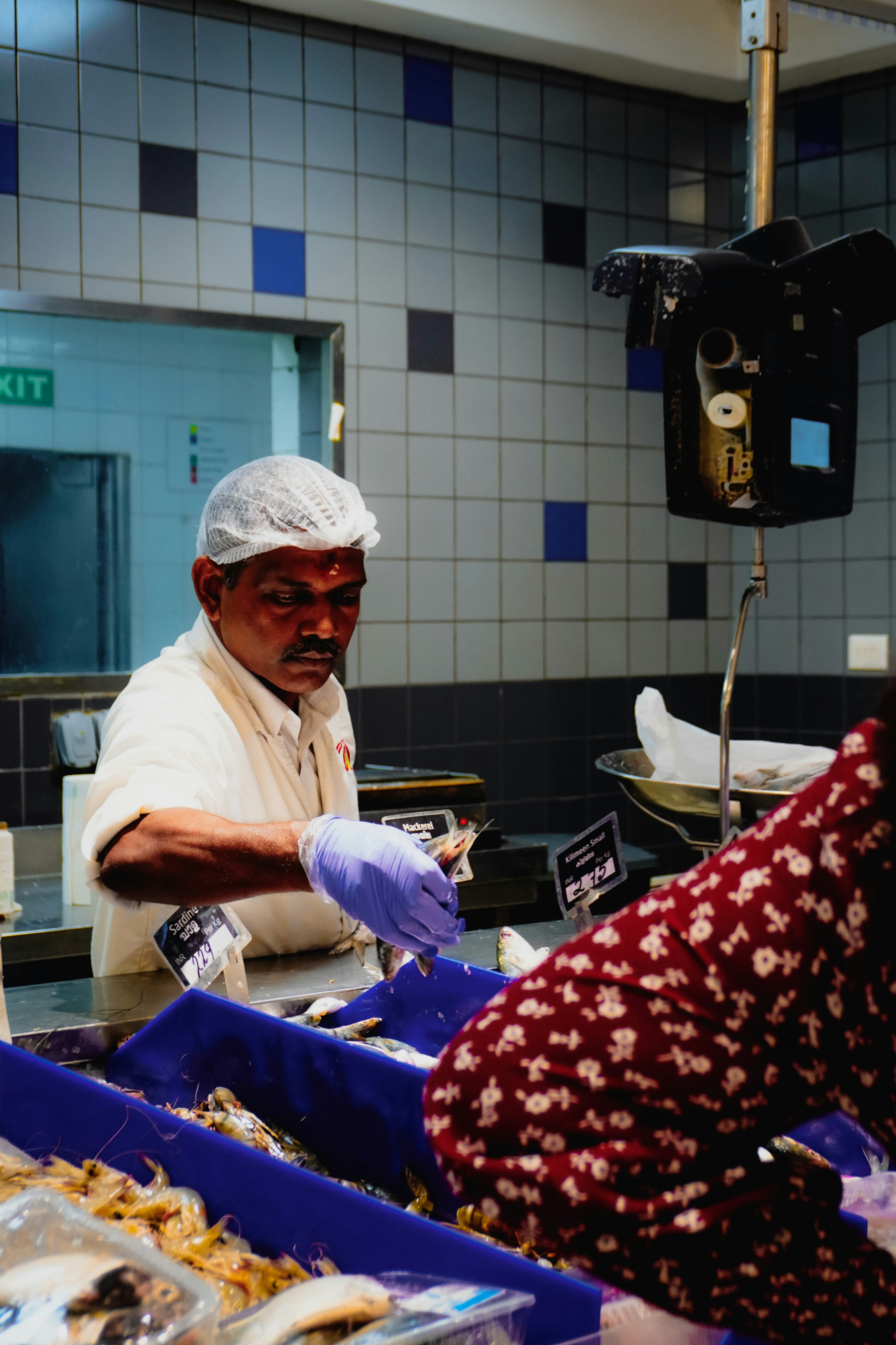 Operator at a market counter prepping seafood under a hanging camera
