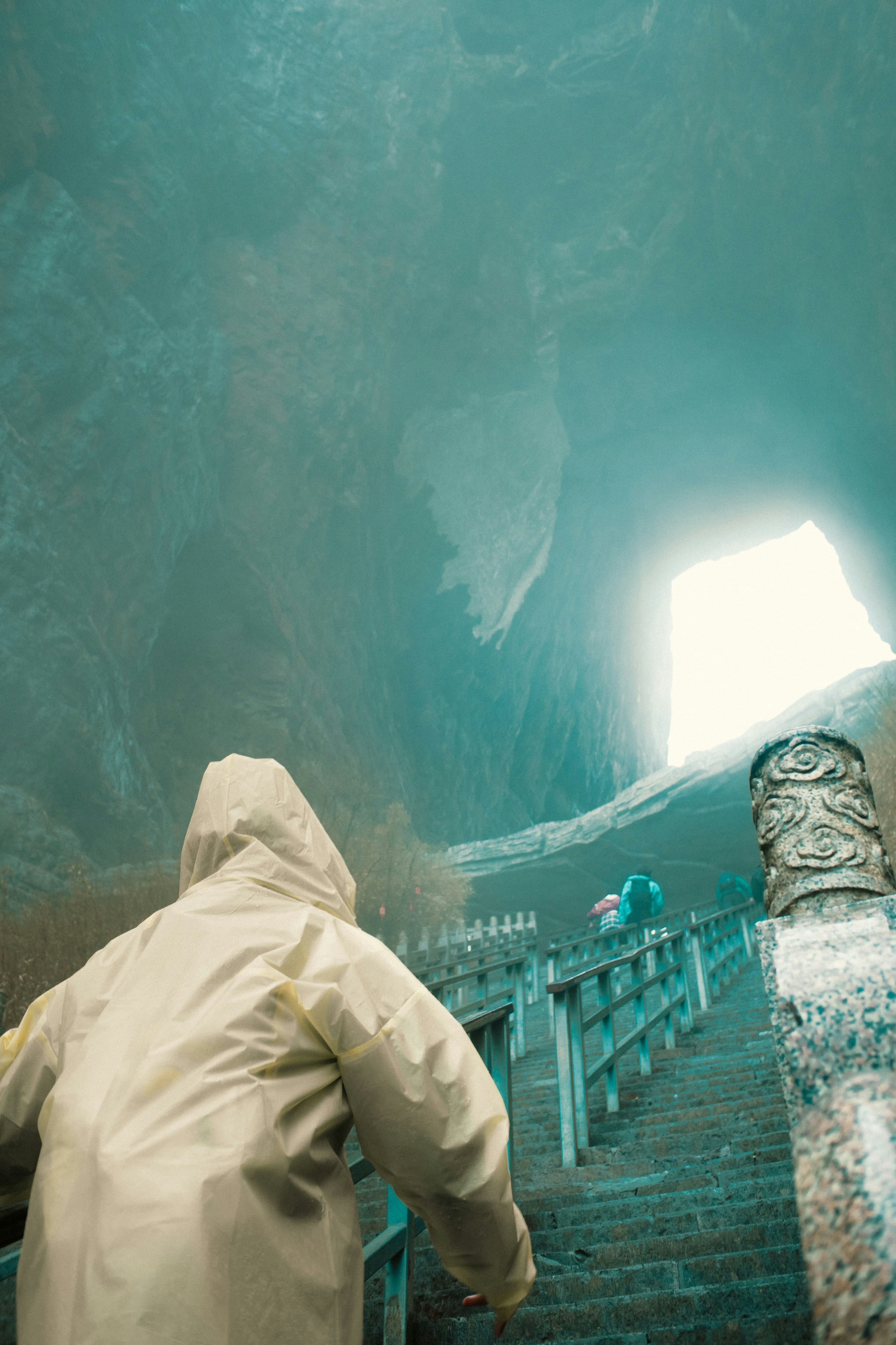 Ascending Toward the Light: A Raincoat Climber in a Cave Staircase