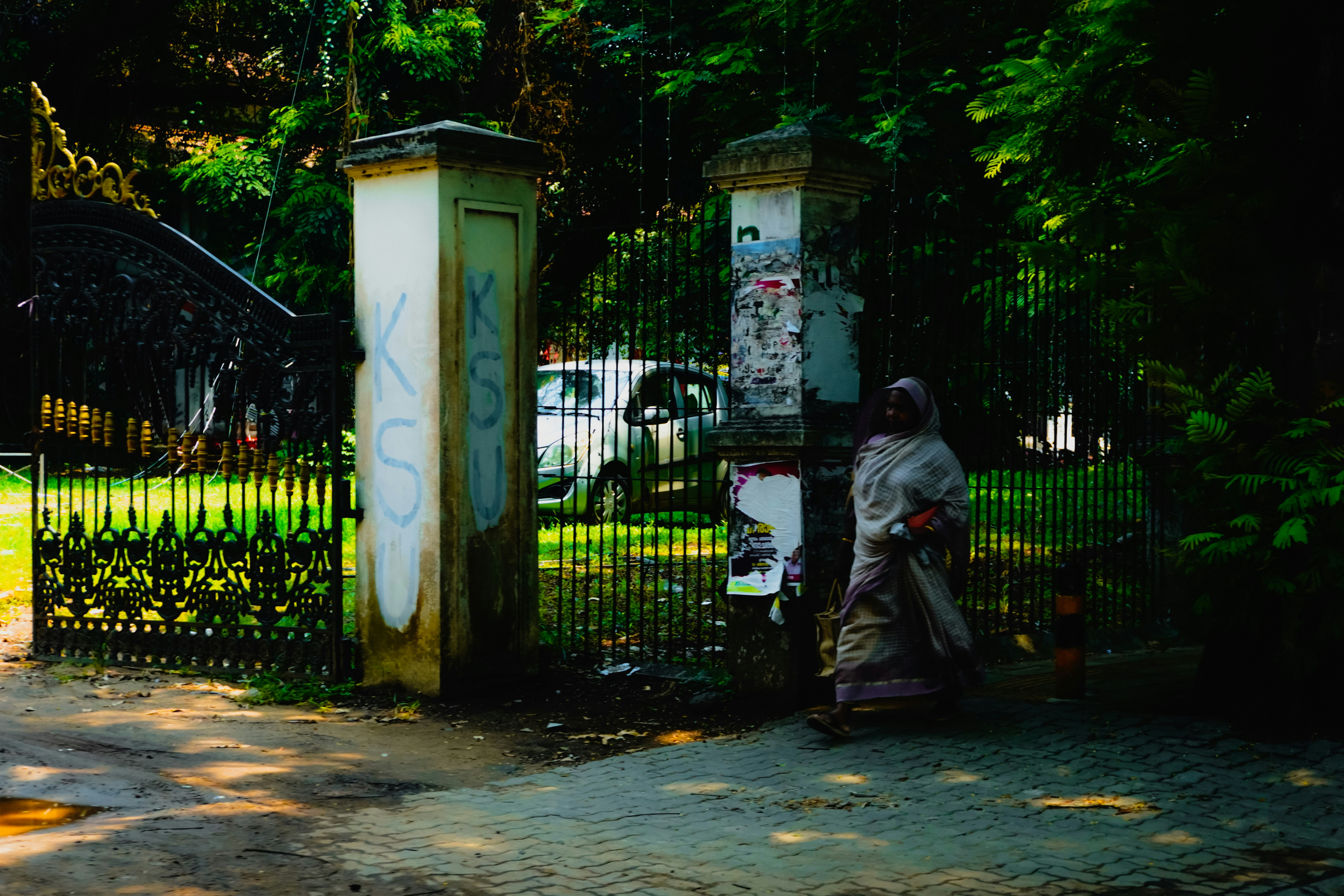 Quiet Gatekeeper: a woman in a shawl passing a mossy fence