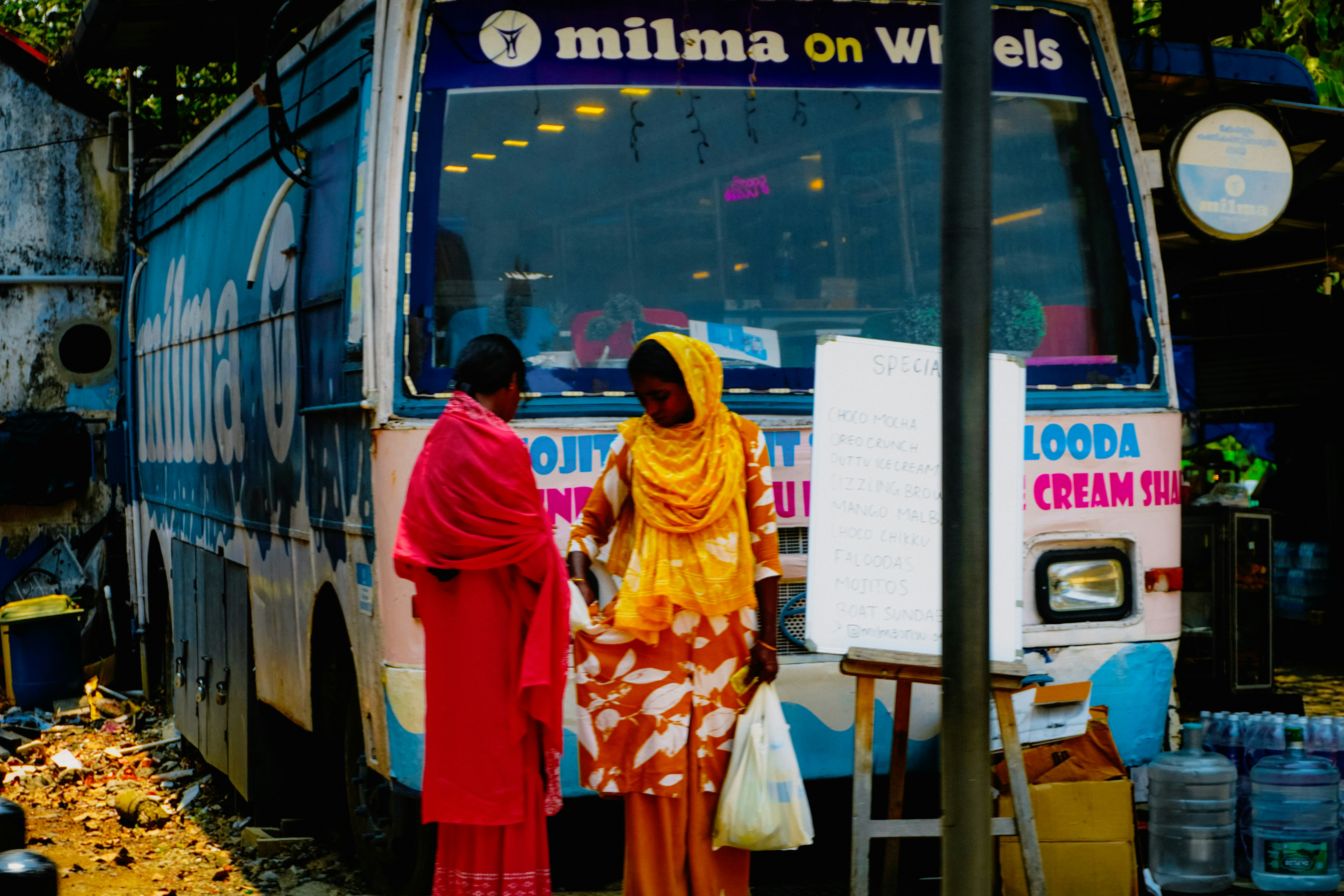 Colors of the Corner: Women in Bright Robes Beside a Bus