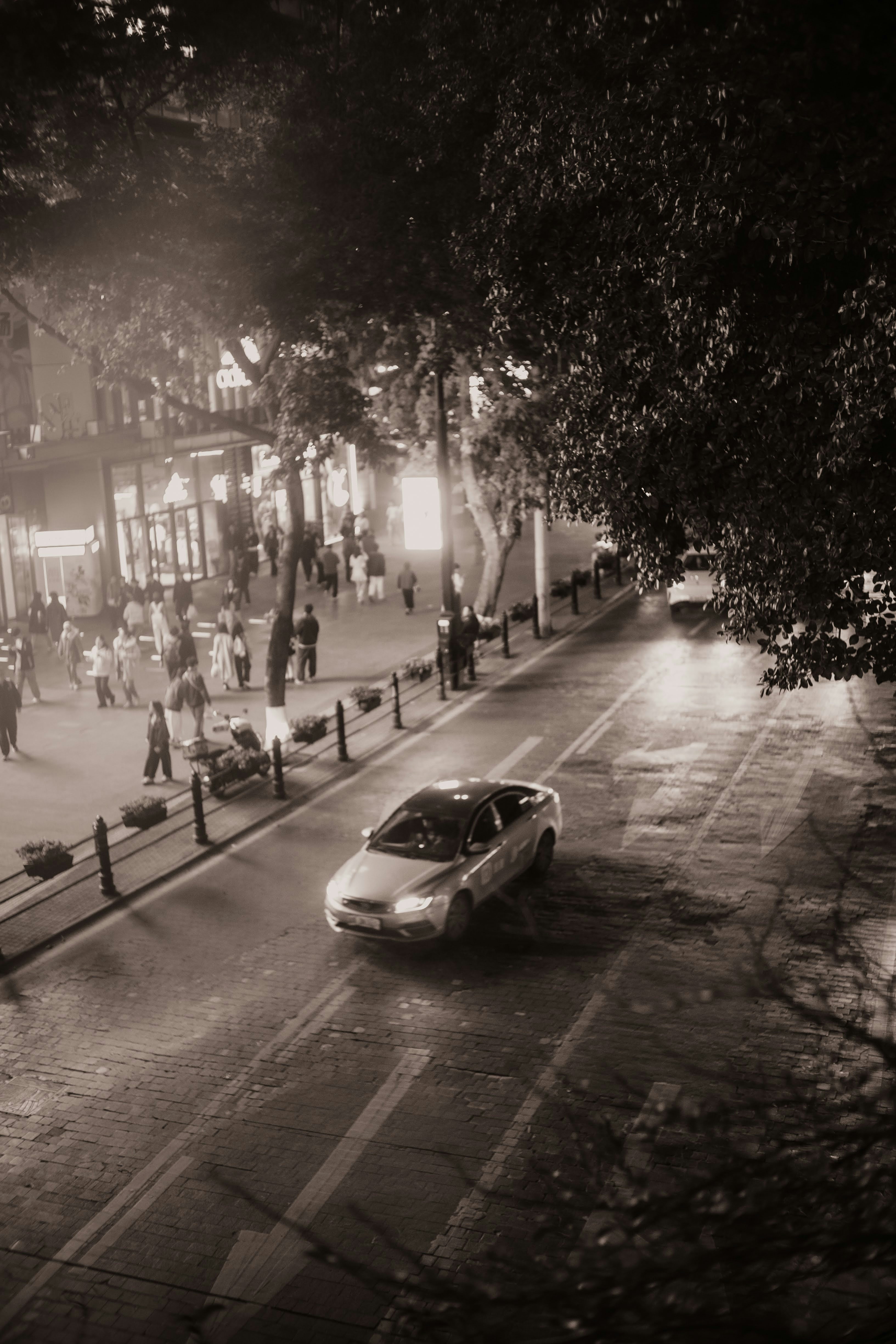 Night Street in Sepia: A Car Stalks Between Pedestrians under Shopfront Lamps