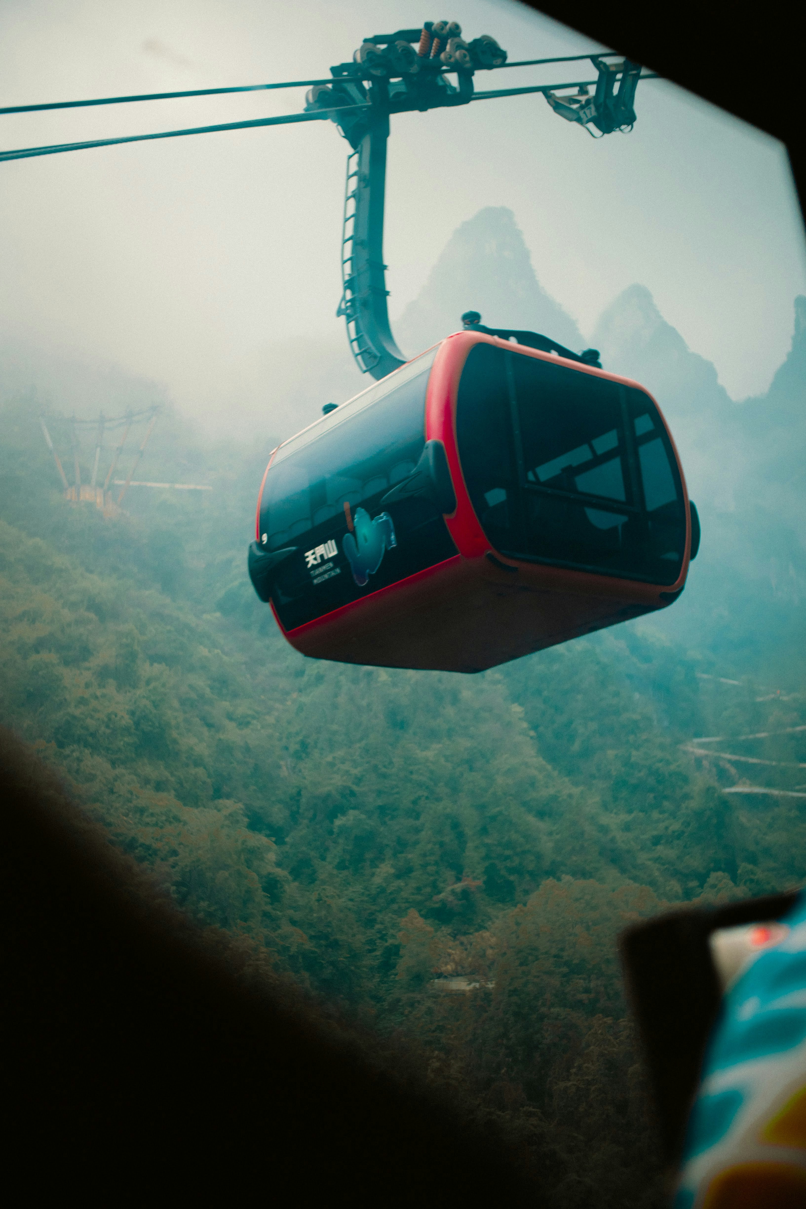 Cable Car Glide: Red Capsule Against Misty Peaks