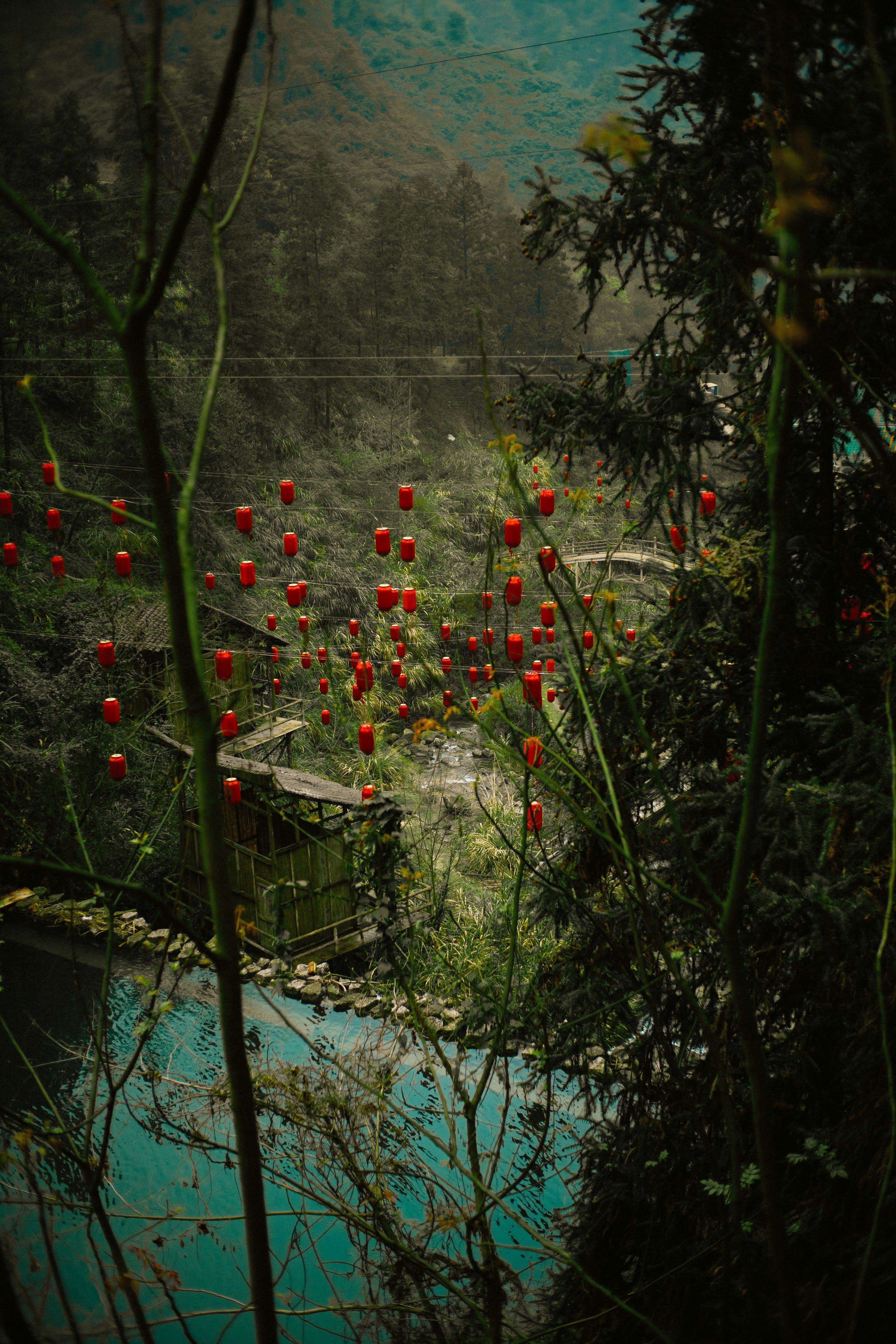 Red lanterns in a misty hillside village by a turquoise river