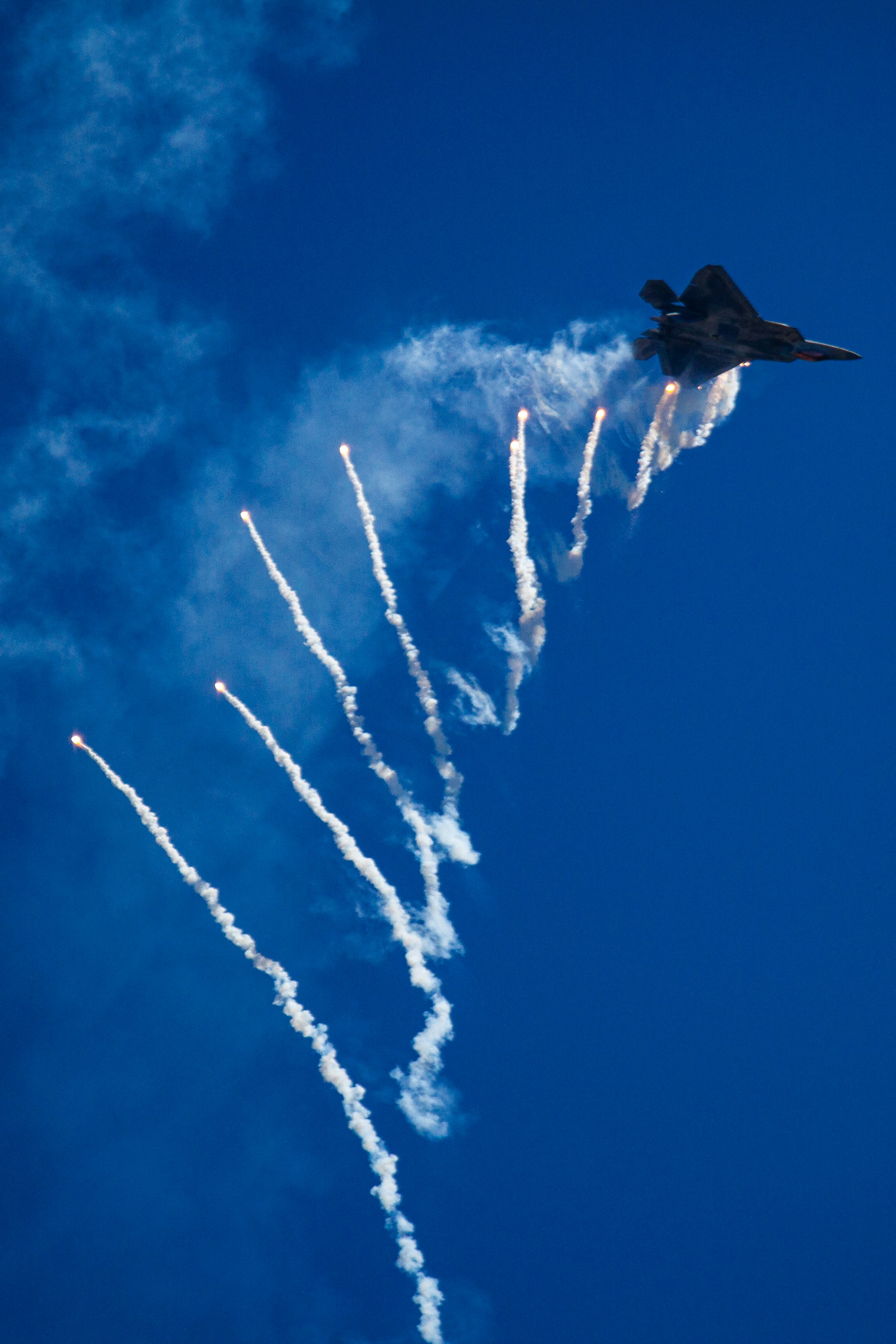 Jet Ascending: Trail of White Flares Against a Deep Blue Sky