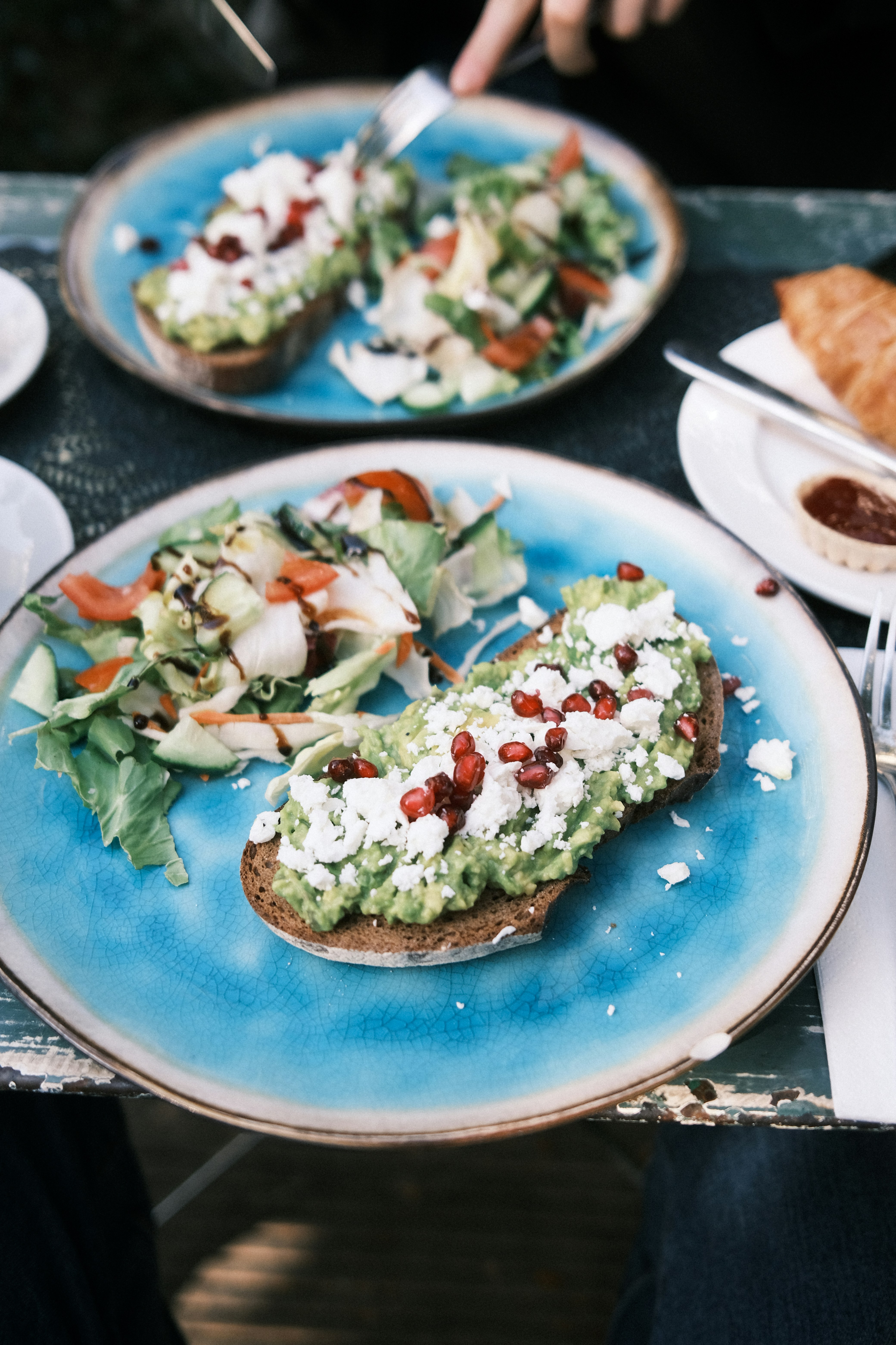 Avocado-sprinkled crostini with herb salad on a sunlit blue plate
