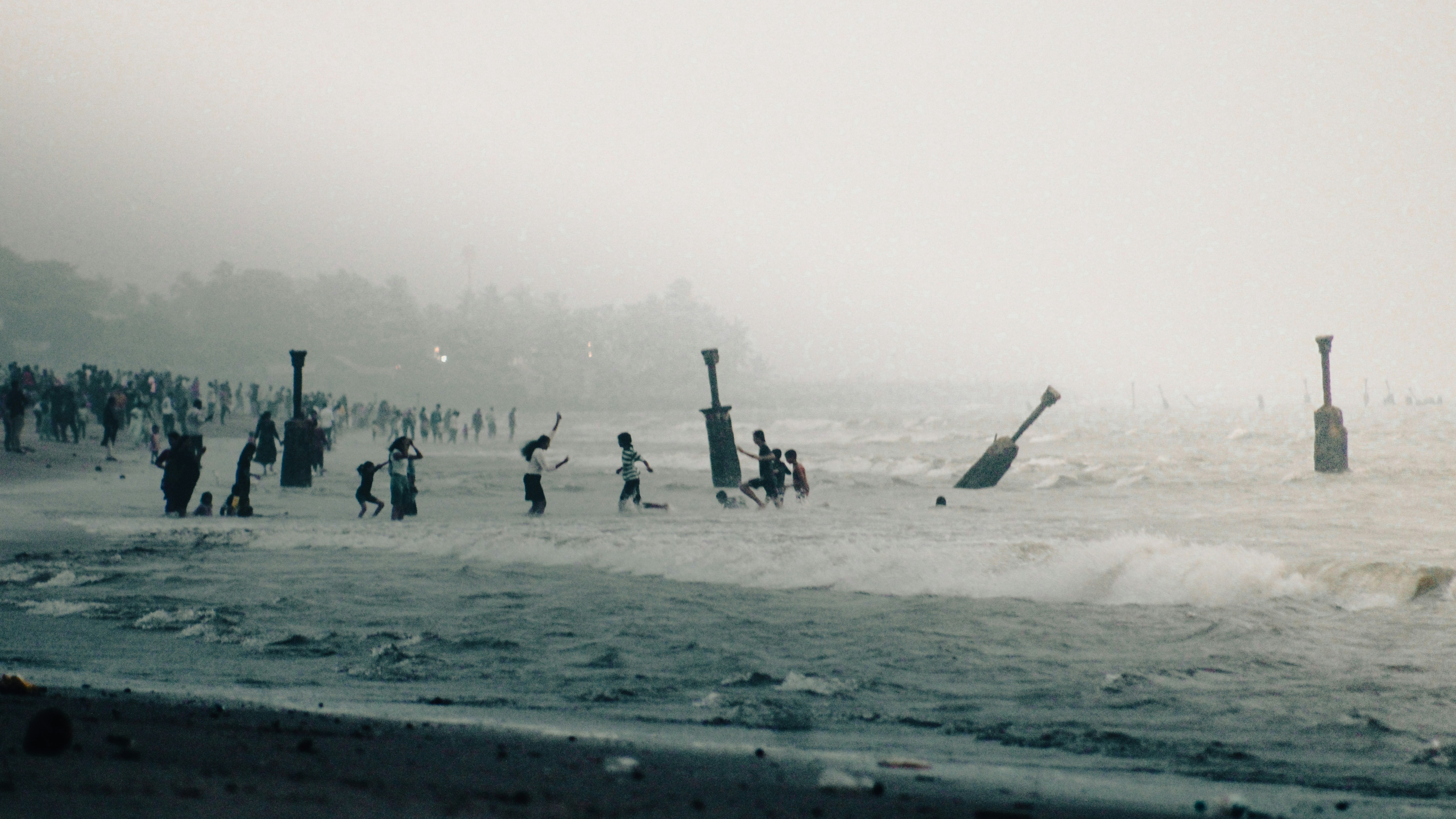Hazy shoreline: silhouettes of beachgoers and drifting pylons