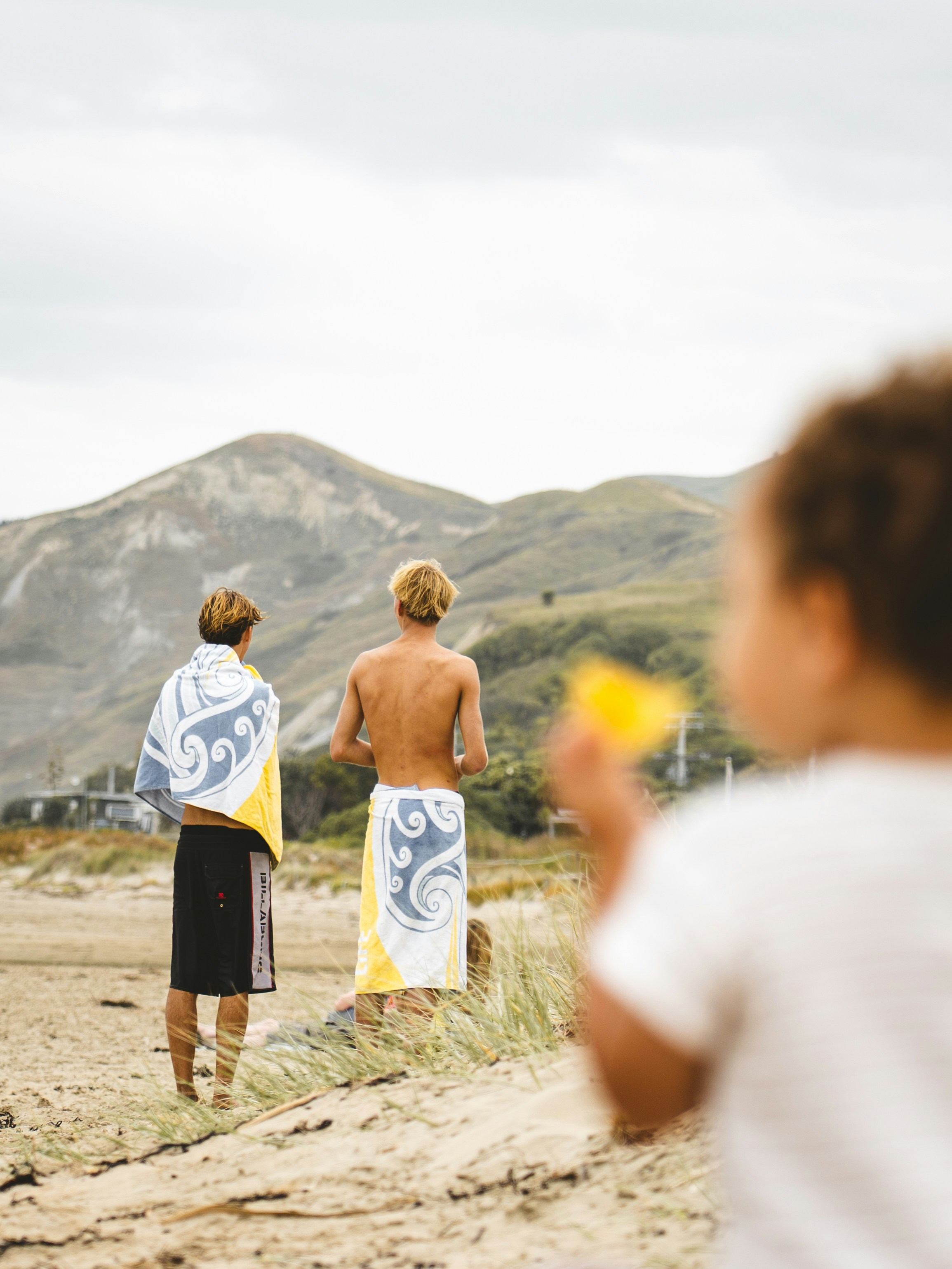 Two surfers on a windswept beach watching the hills