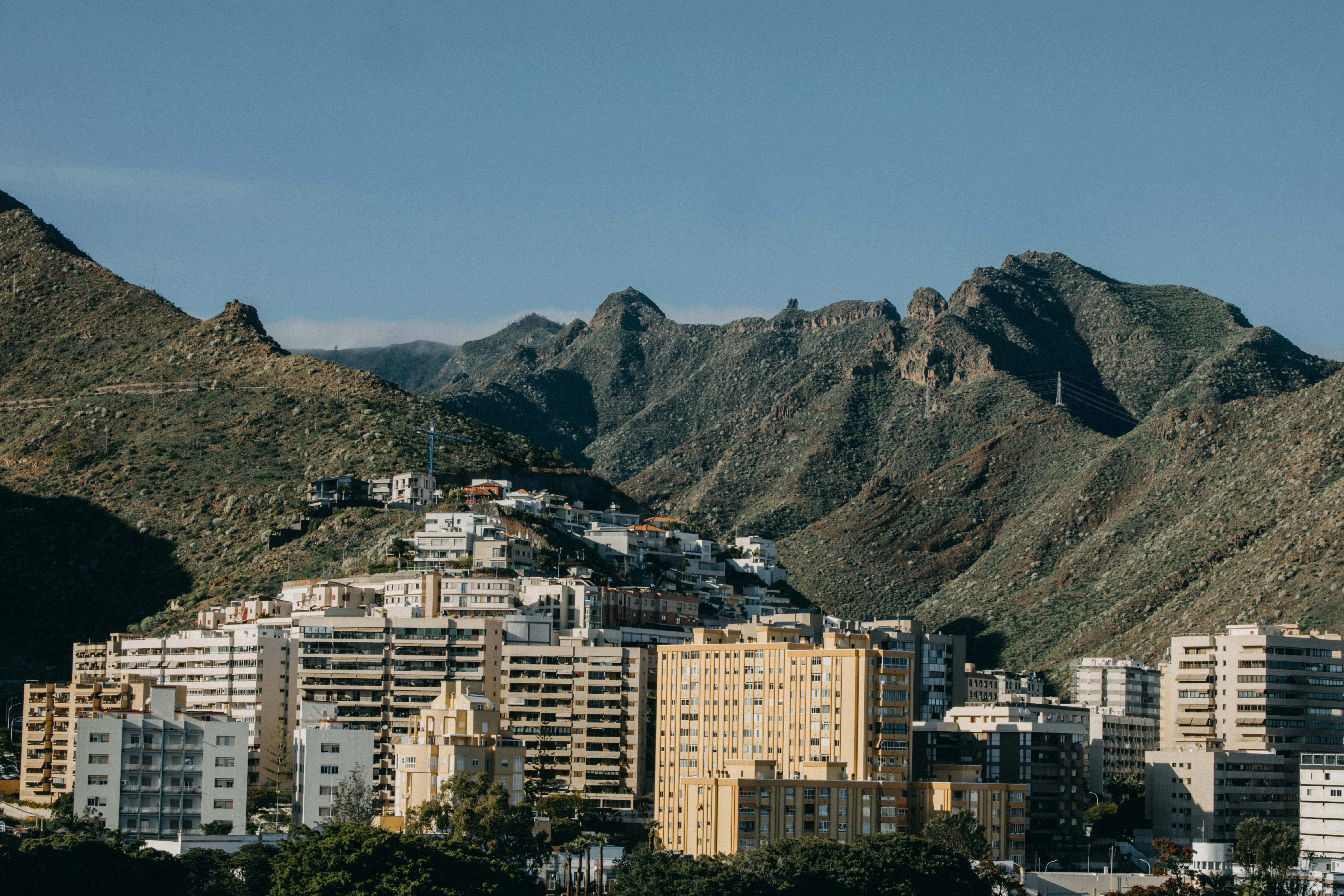 Urban Cliffline: Buildings Nestle Into Mountain Range Under Clear Blue Sky