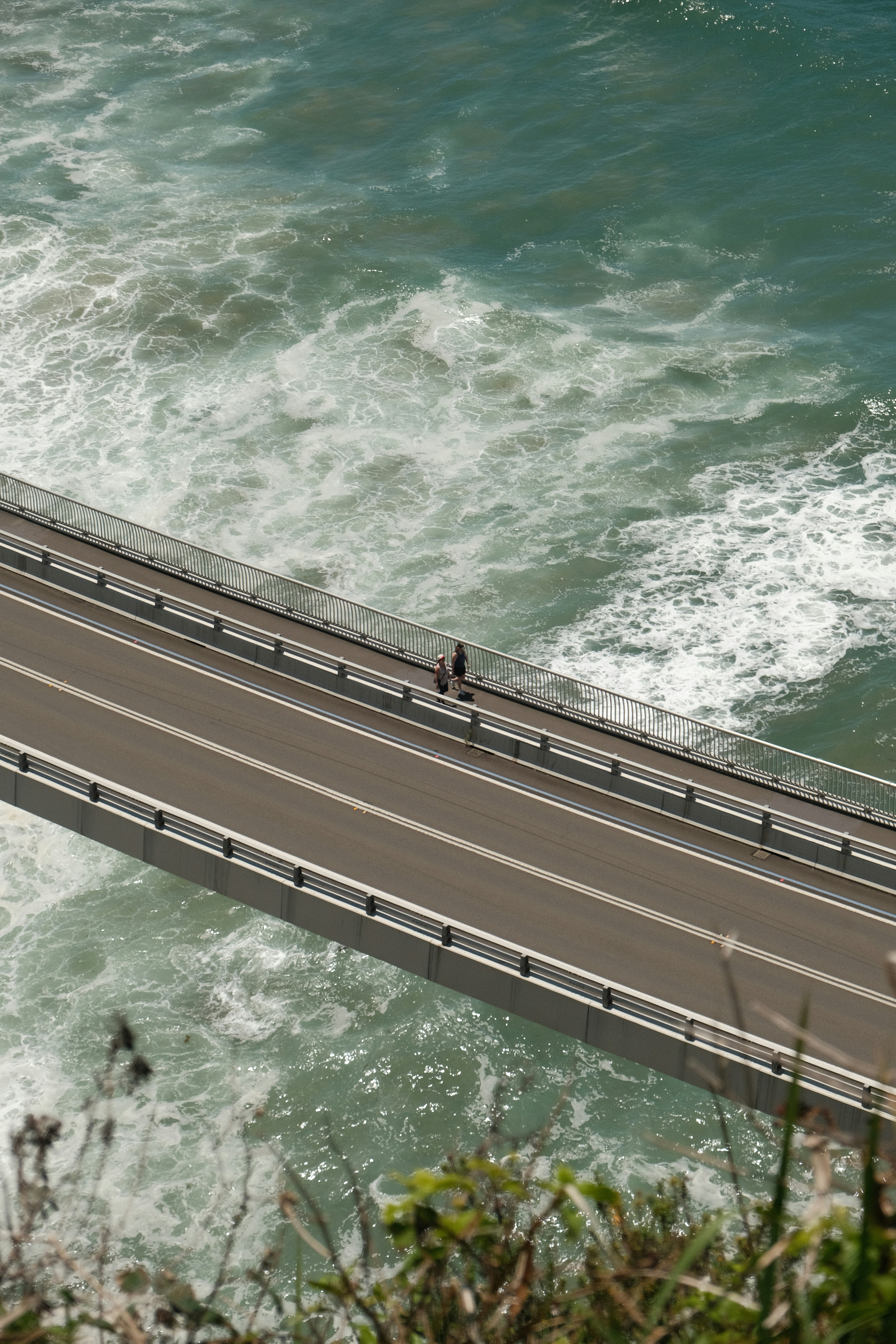 Edge of the Sea: Pedestrians on a Narrow Bridge Carved Across Turbulent White Coast