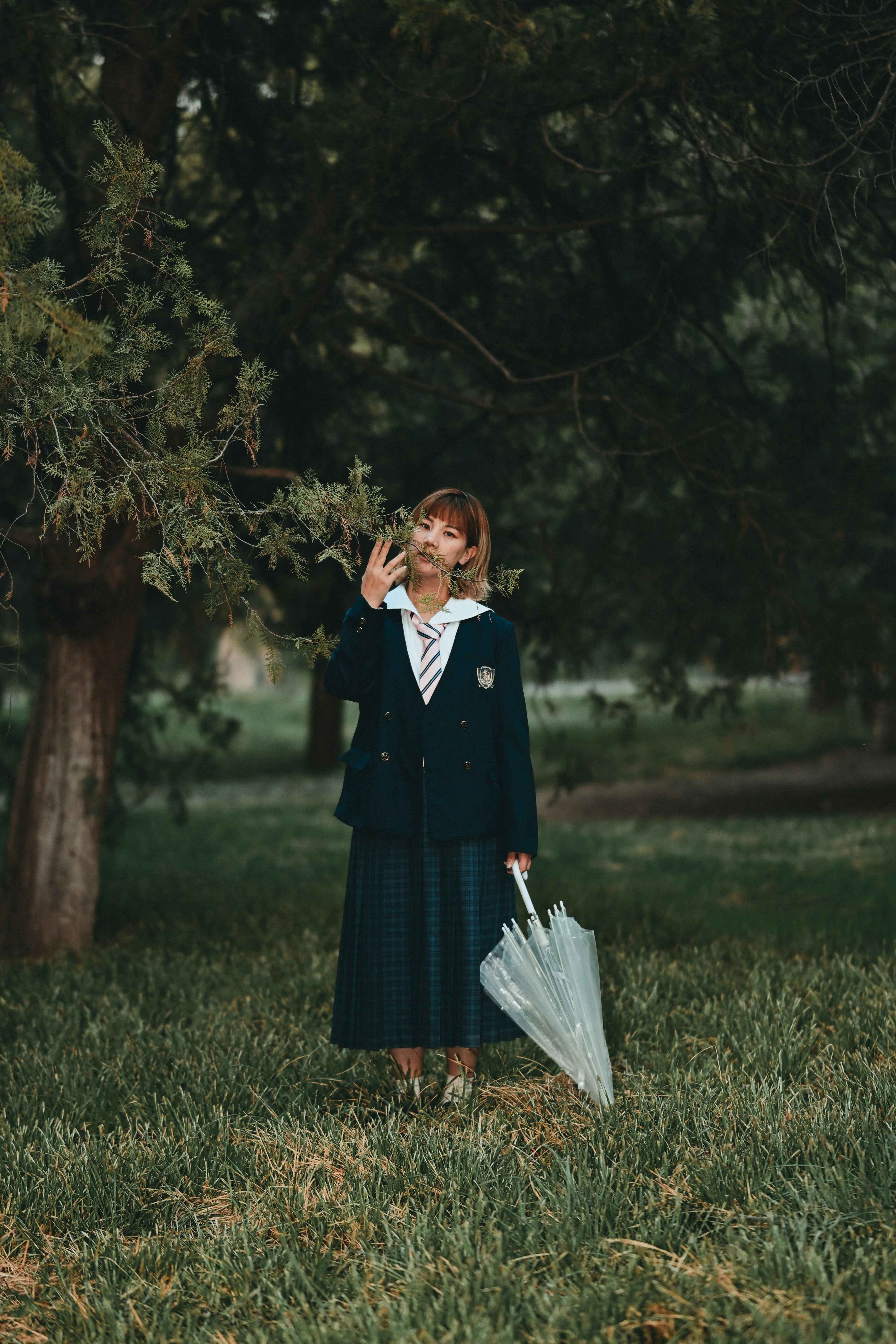 Girl in a navy school uniform among pines, holding a white umbrella