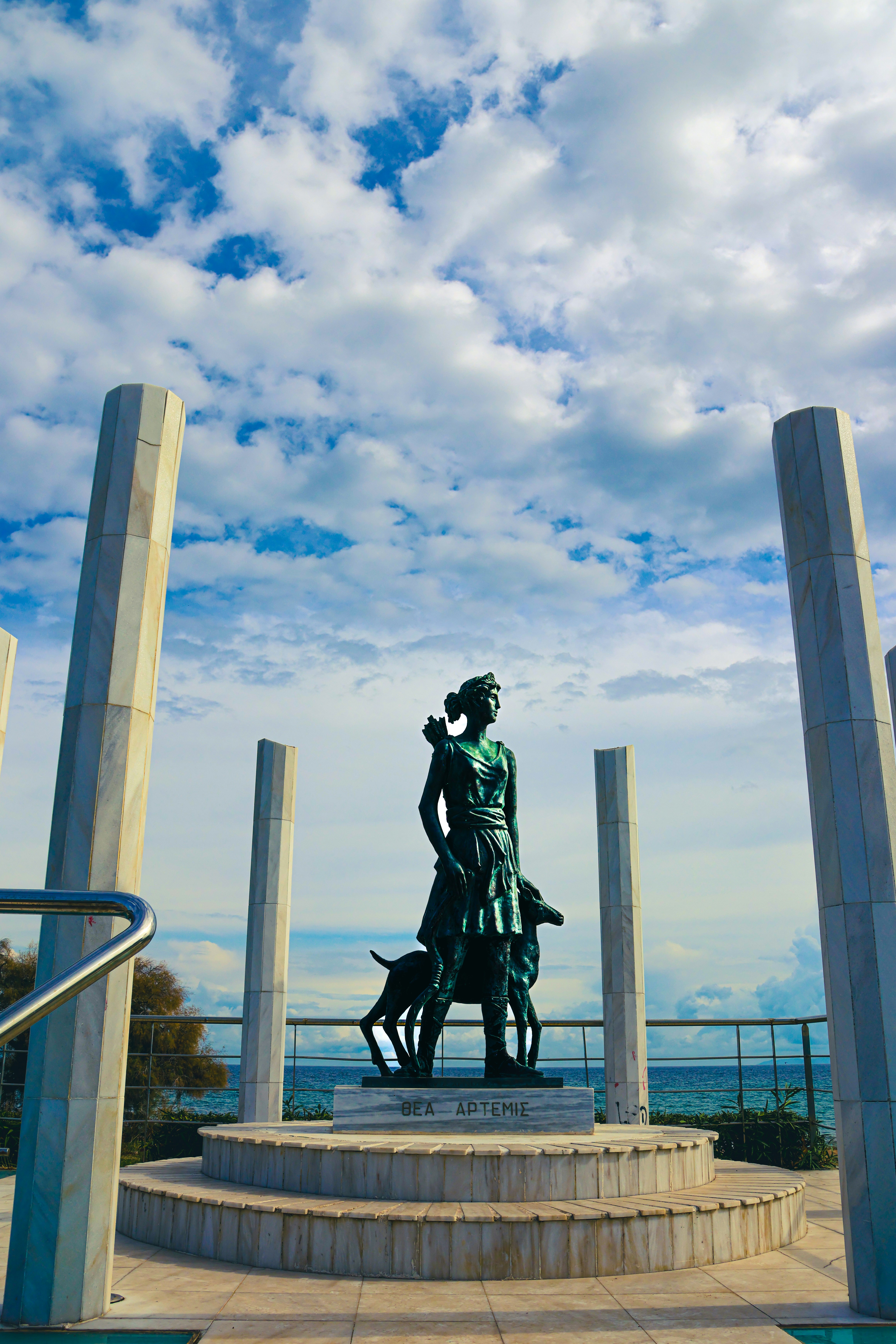 Statue at the Edge: A Bronze Figure Beneath a Sky of Clouds