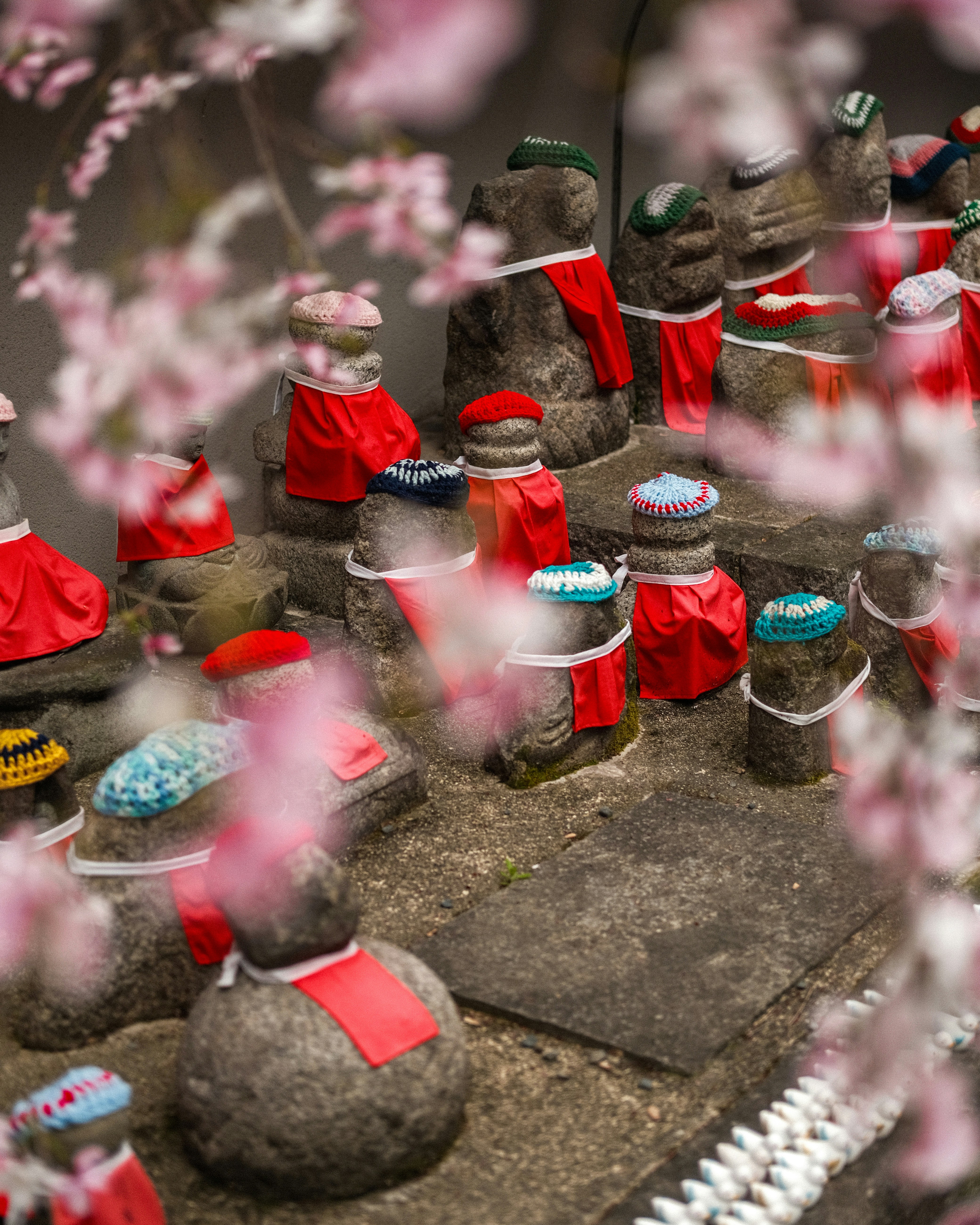Row of red-cloaked statues at a tranquil shrine with pink blossoms