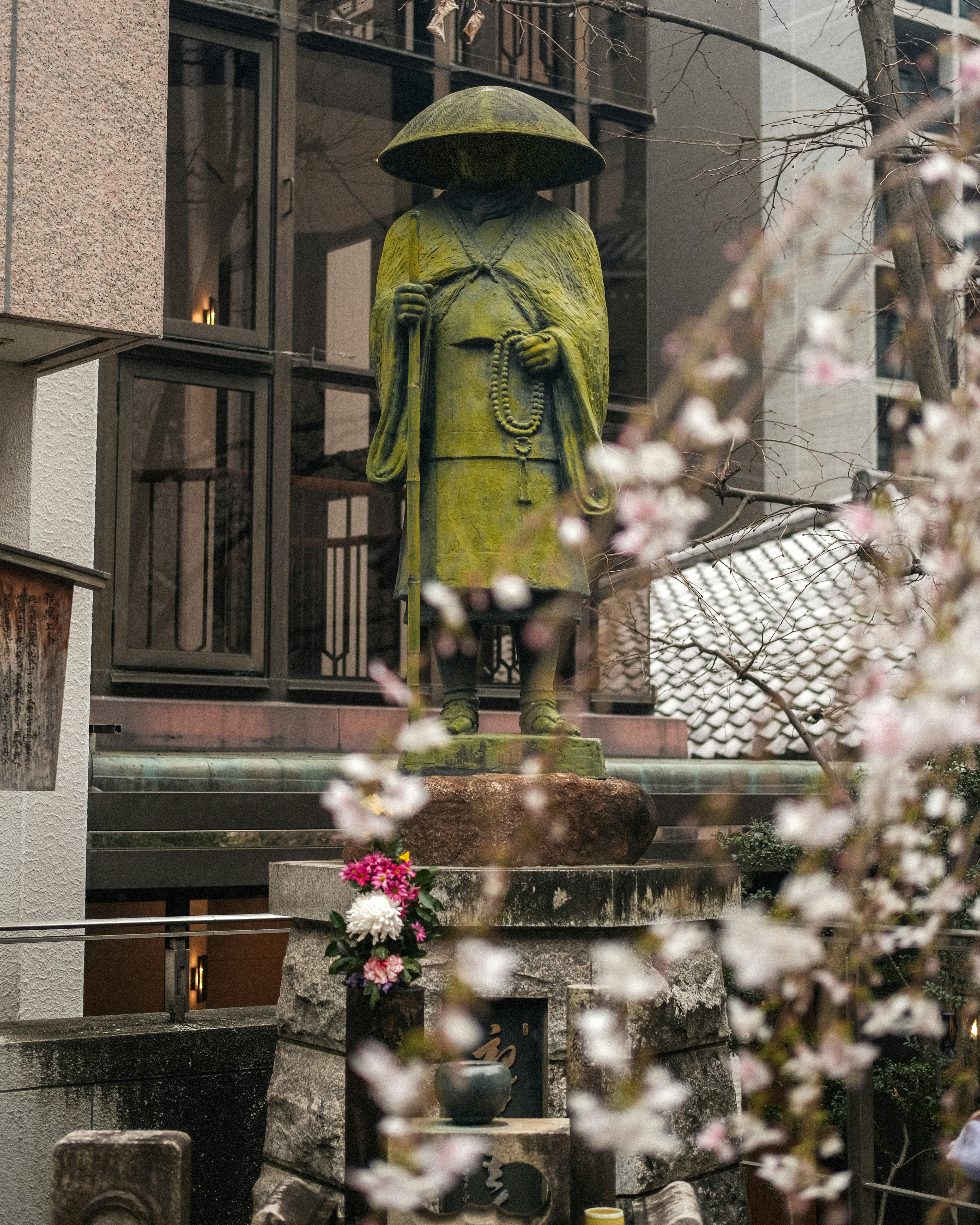 Green Bodhisattva Amid Sakura Blooms in Urban Shrine