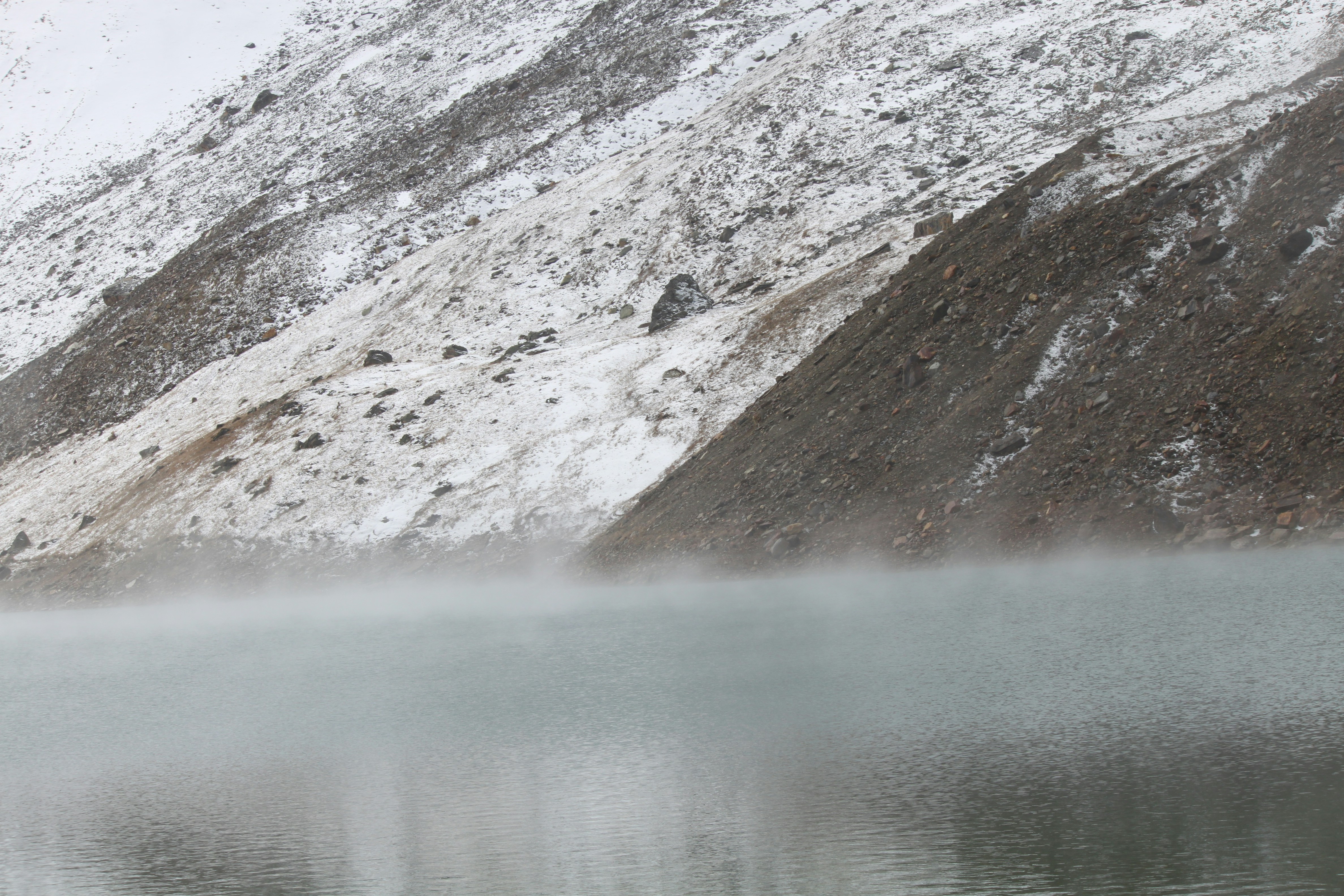 Mist over the glacial lagoon at the foot of slate-gray slopes