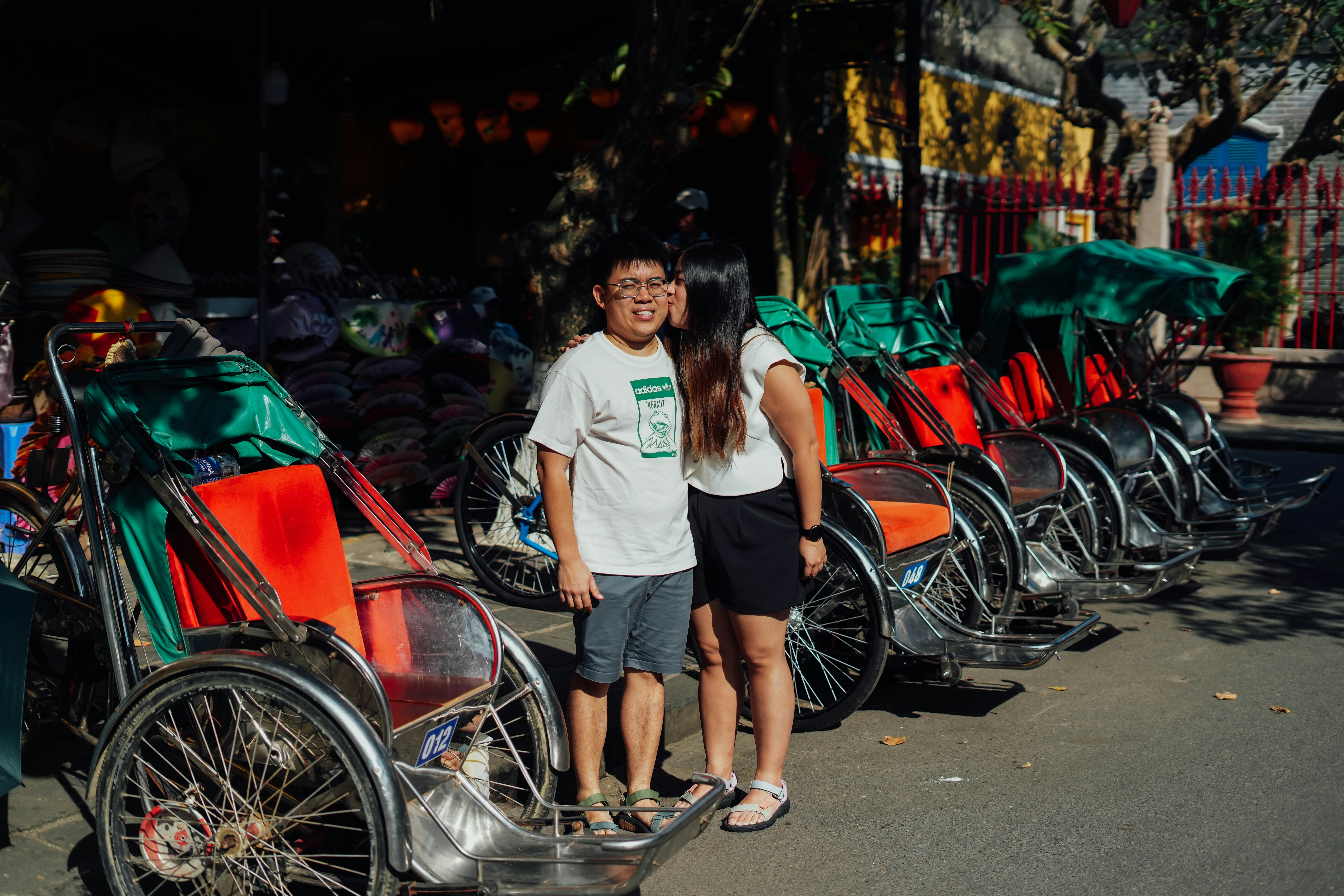 Two Tourists Pause Amid Colorful Pedicabs Under a Sunlit Lane