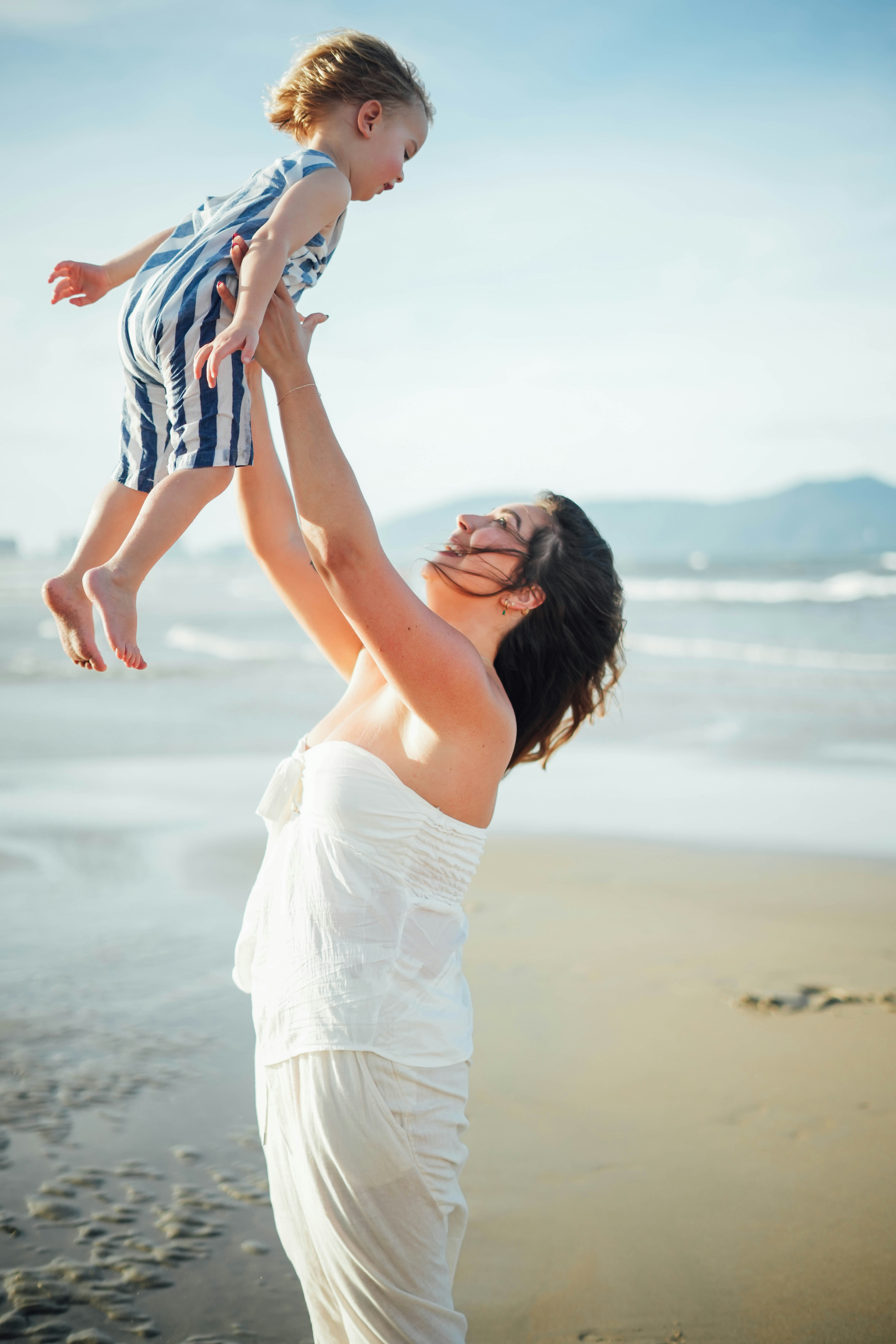 Joyful Lift: A Beach Moment of Maternal Play