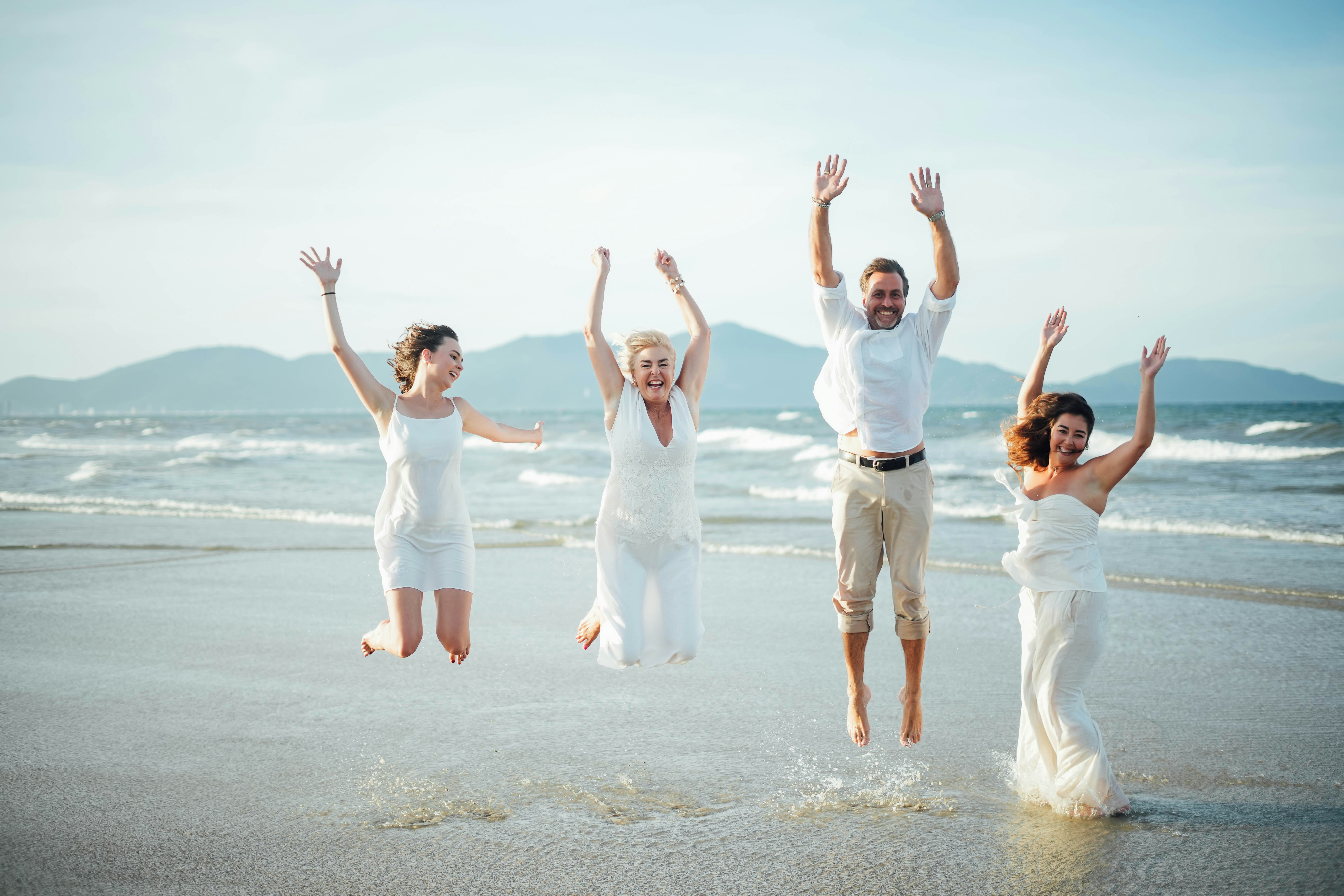 Joyful leap: four friends rise from the tide in white on a sunlit seashore