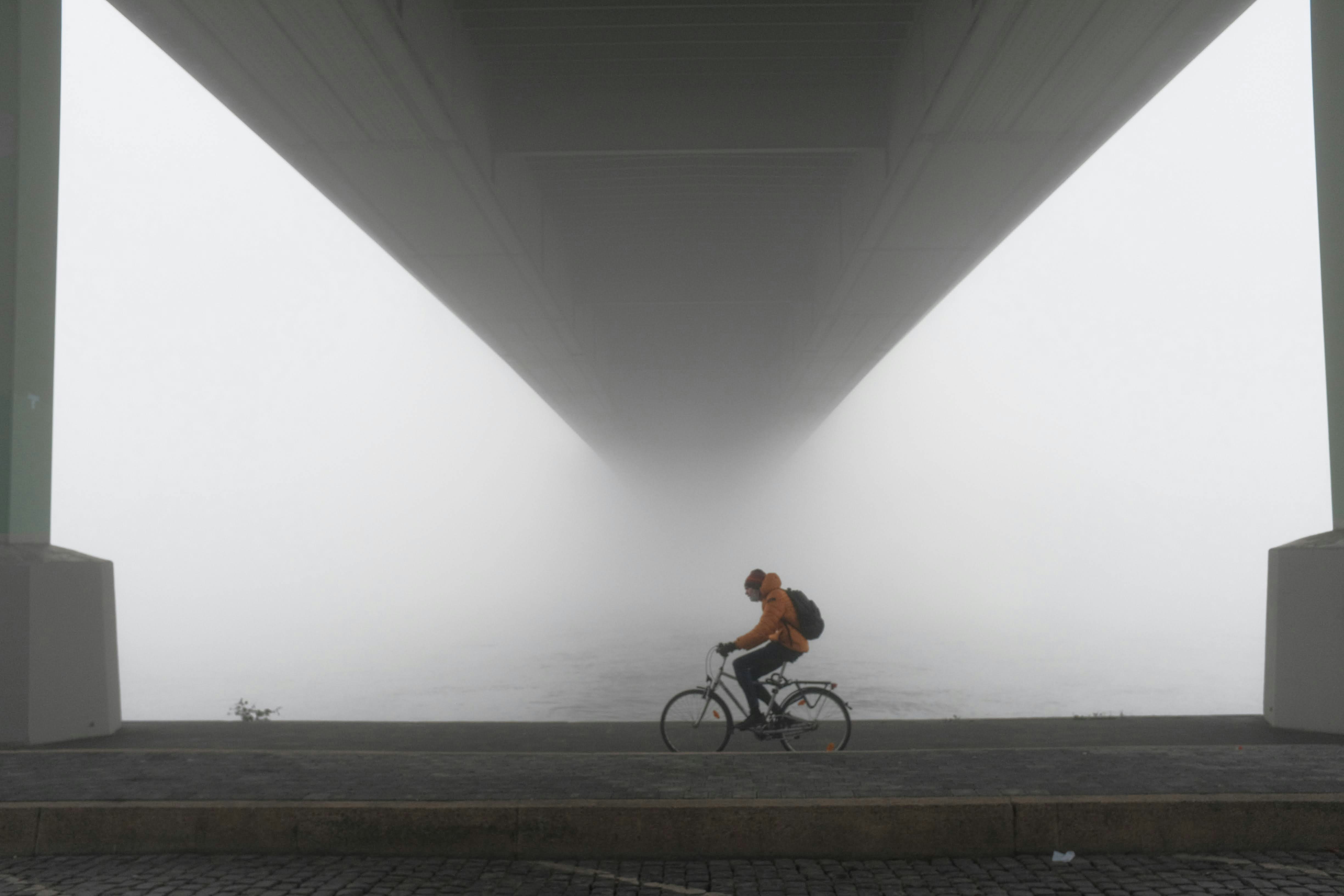 Cyclist under a foggy overpass: solitude in motion