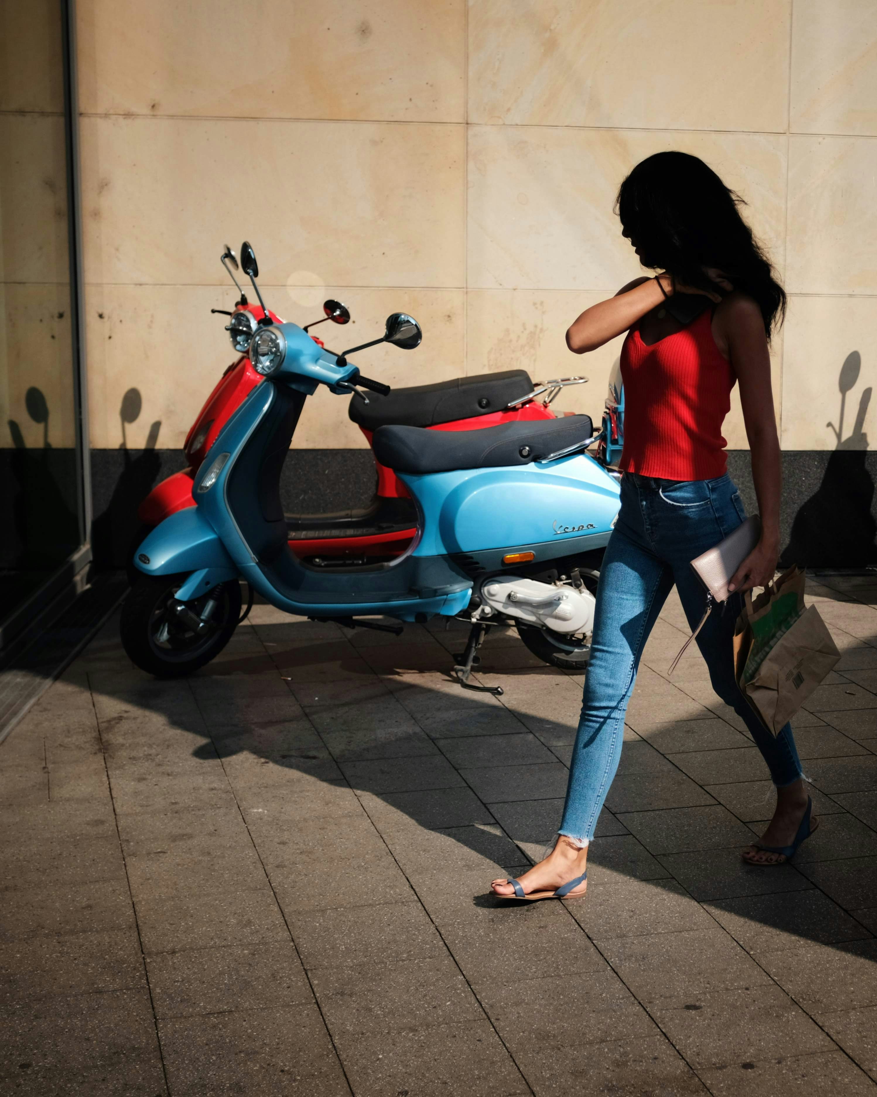 Red-Top Walk: A Woman Passes a Blue Scooter in Morning Light