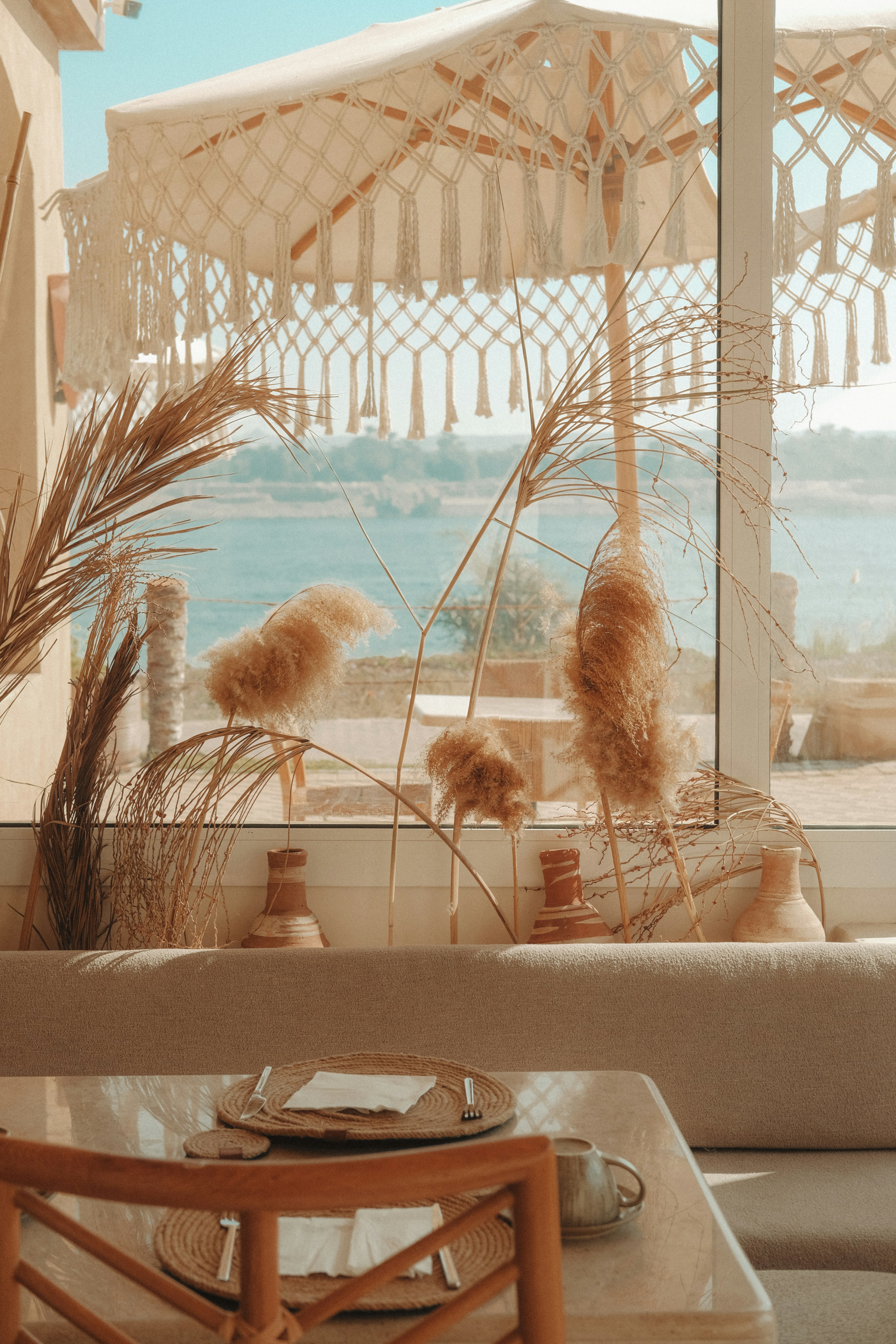Cozy coastal cafe by the river with ornamental grasses and sunlit wicker decor