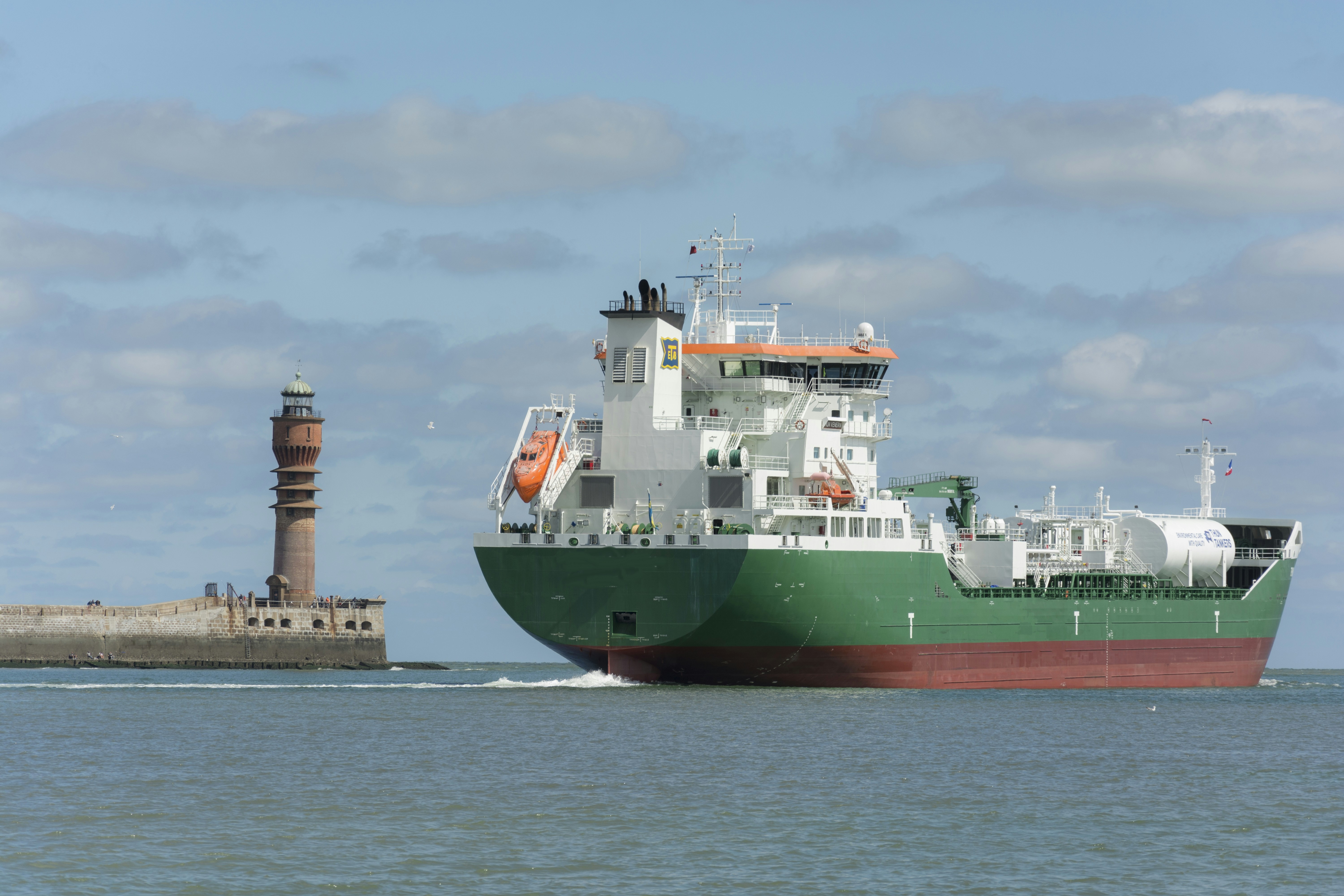 Coastal Passage: A Green-Hulled Carrier Ridges the Sea Near a Lighthouse