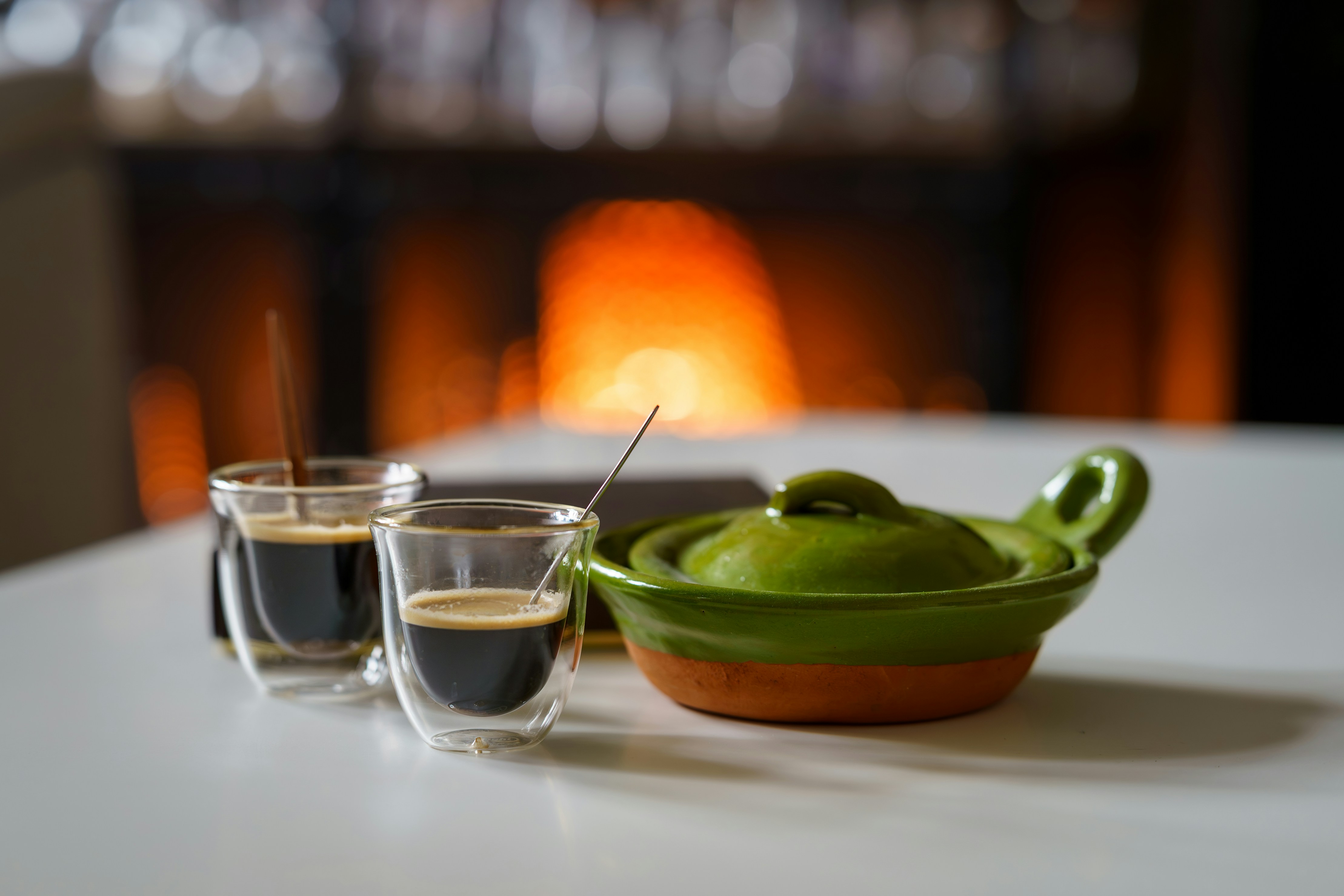 Quiet warmth: espresso trio beside a green ceramic dish by a glowing hearth