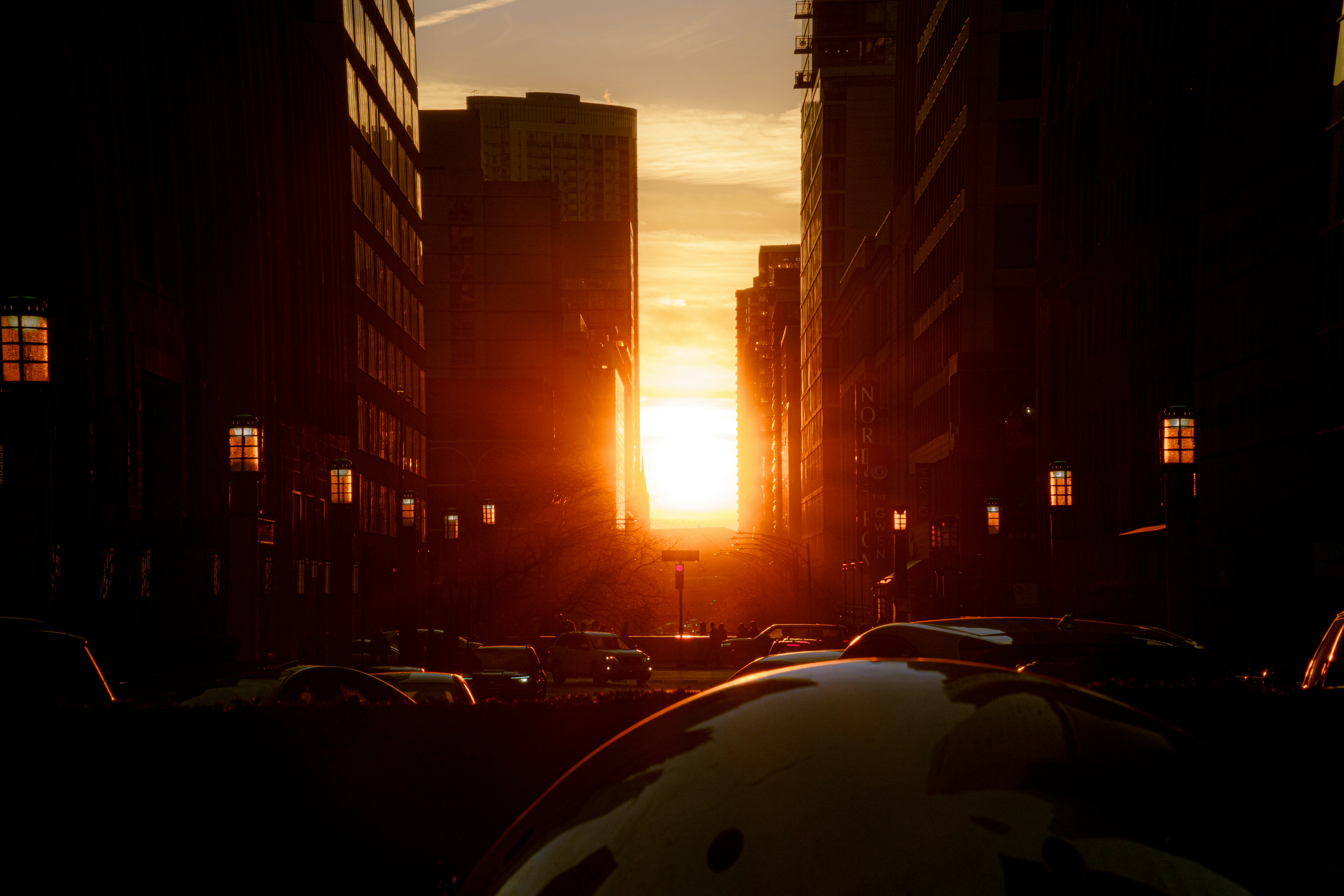 Golden sunset pours between tall buildings, illuminating the street and a glossy dome in the foreground.