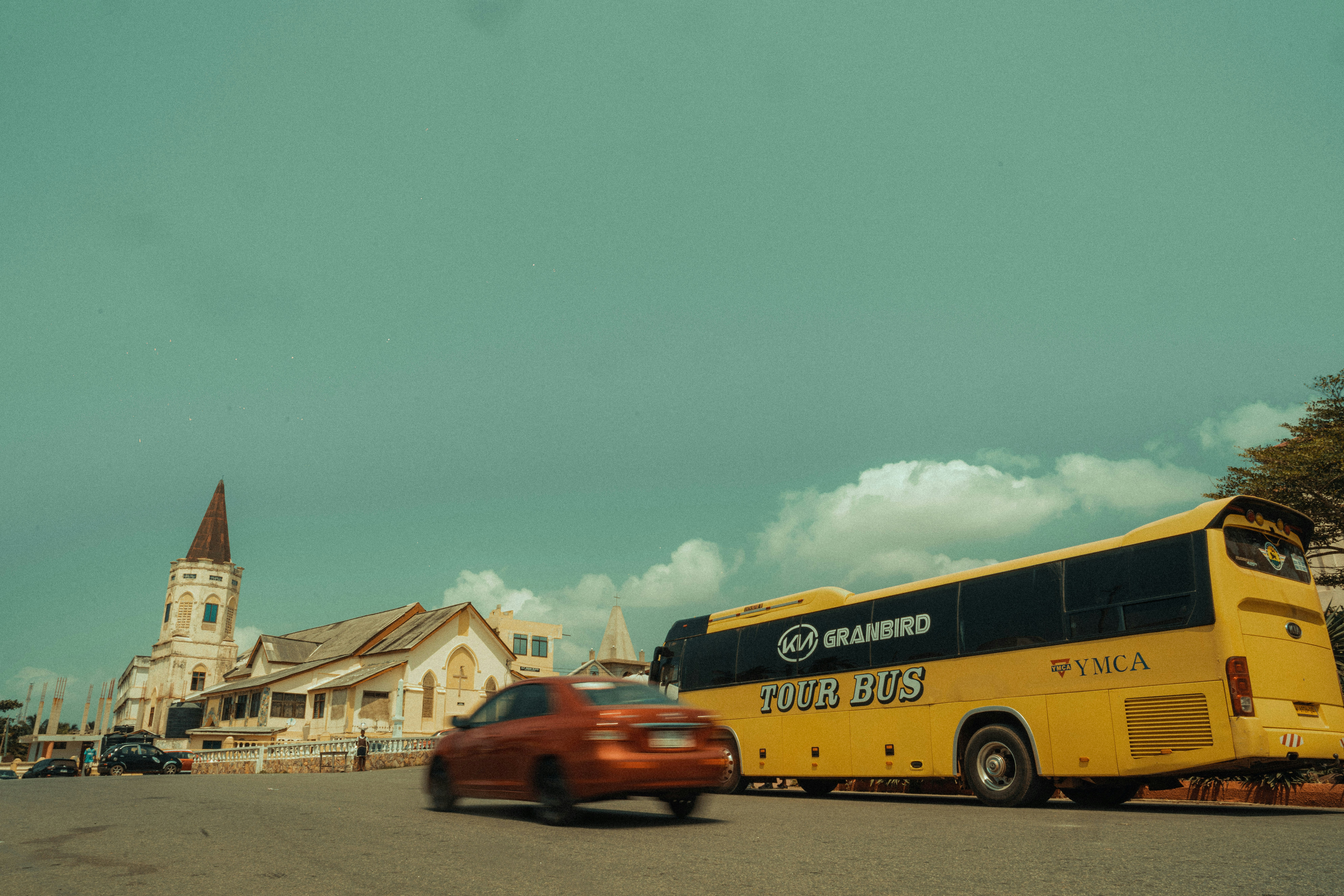 Sunlit Street Scene with a Bright Yellow Tour Bus and Blurred Red Car