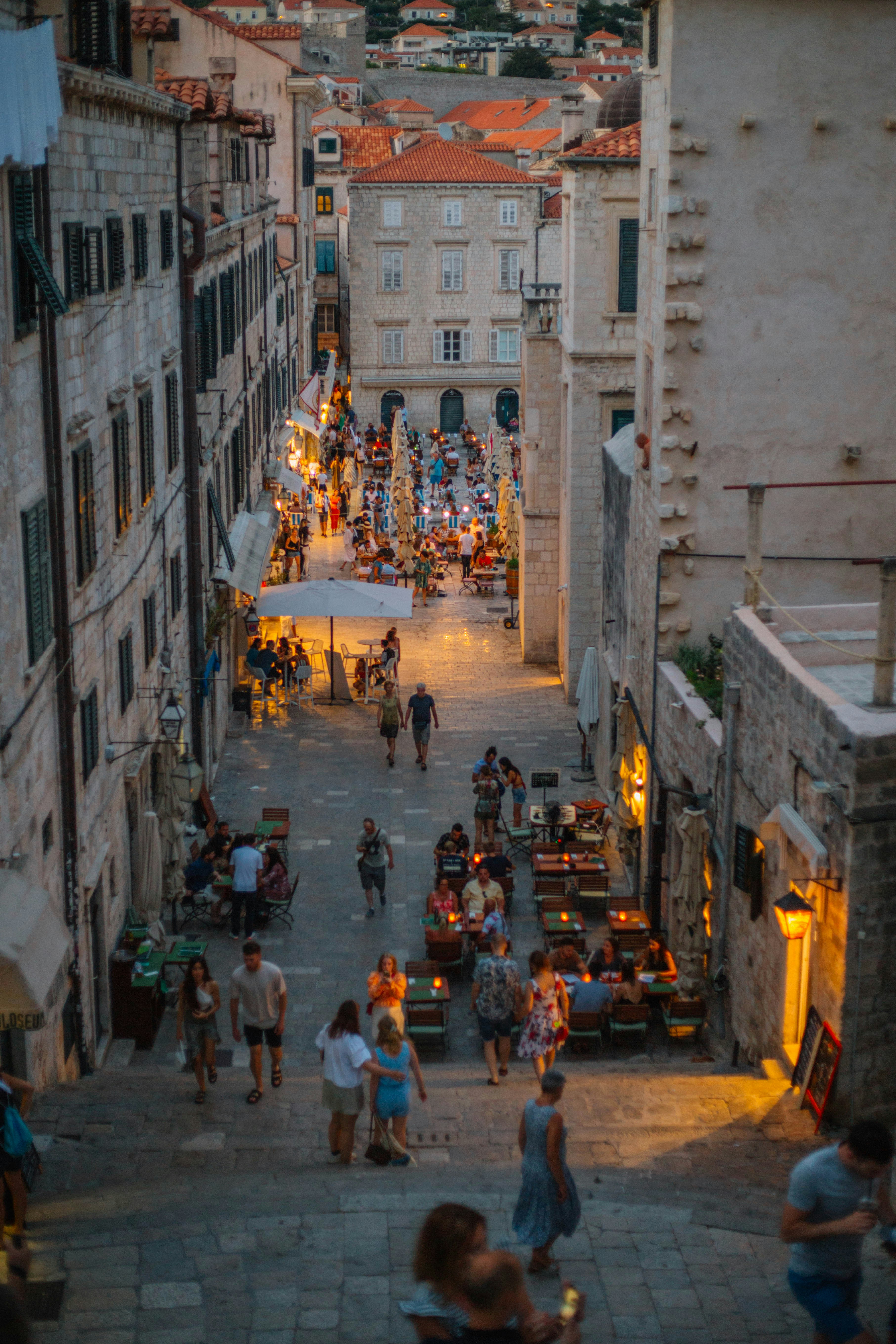 Stone alleyway bistro lights guide a sunlit evening crowd