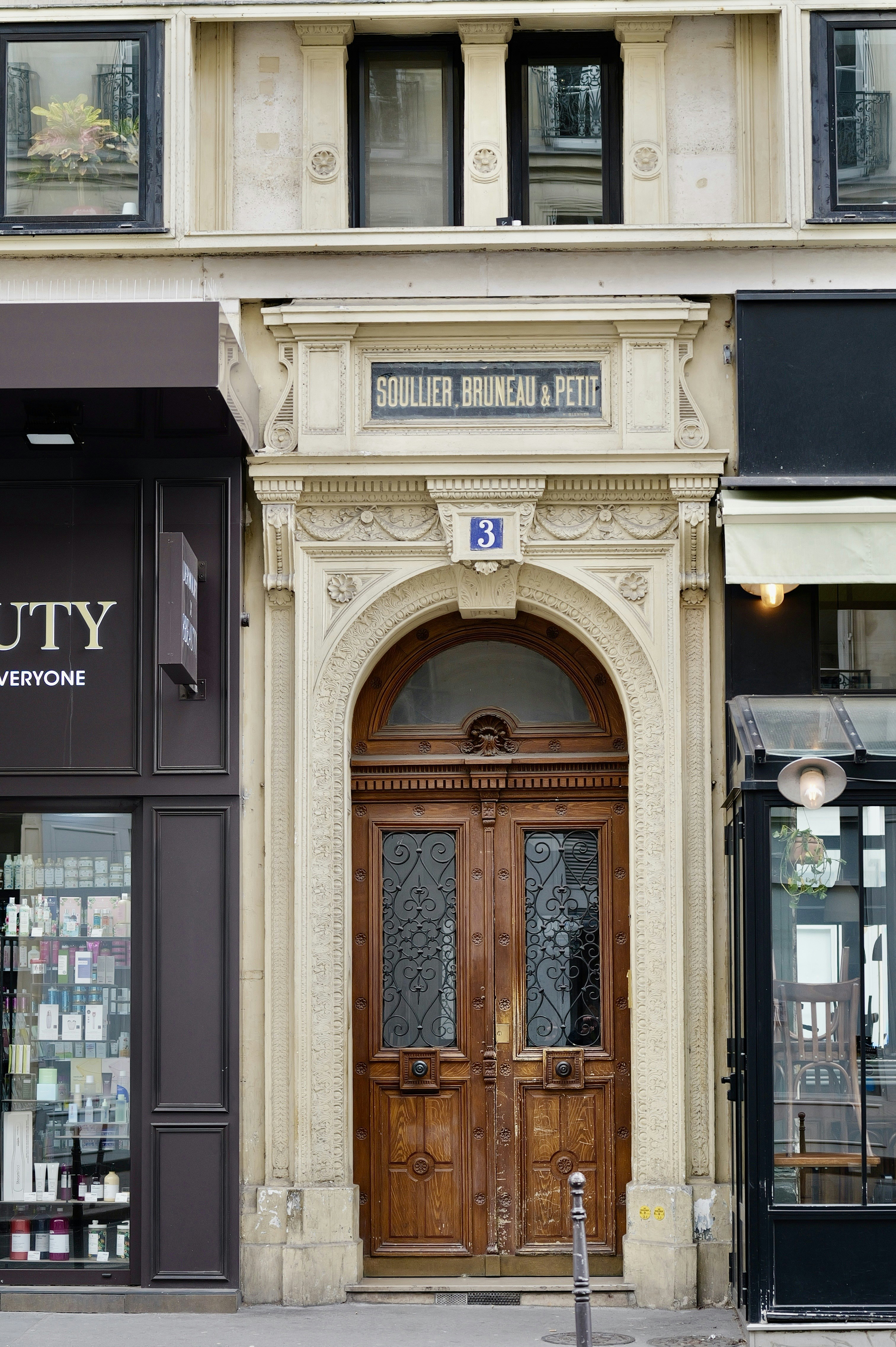 Ornate doorway of a Parisian storefront framed by glass-fronted neighboring shops