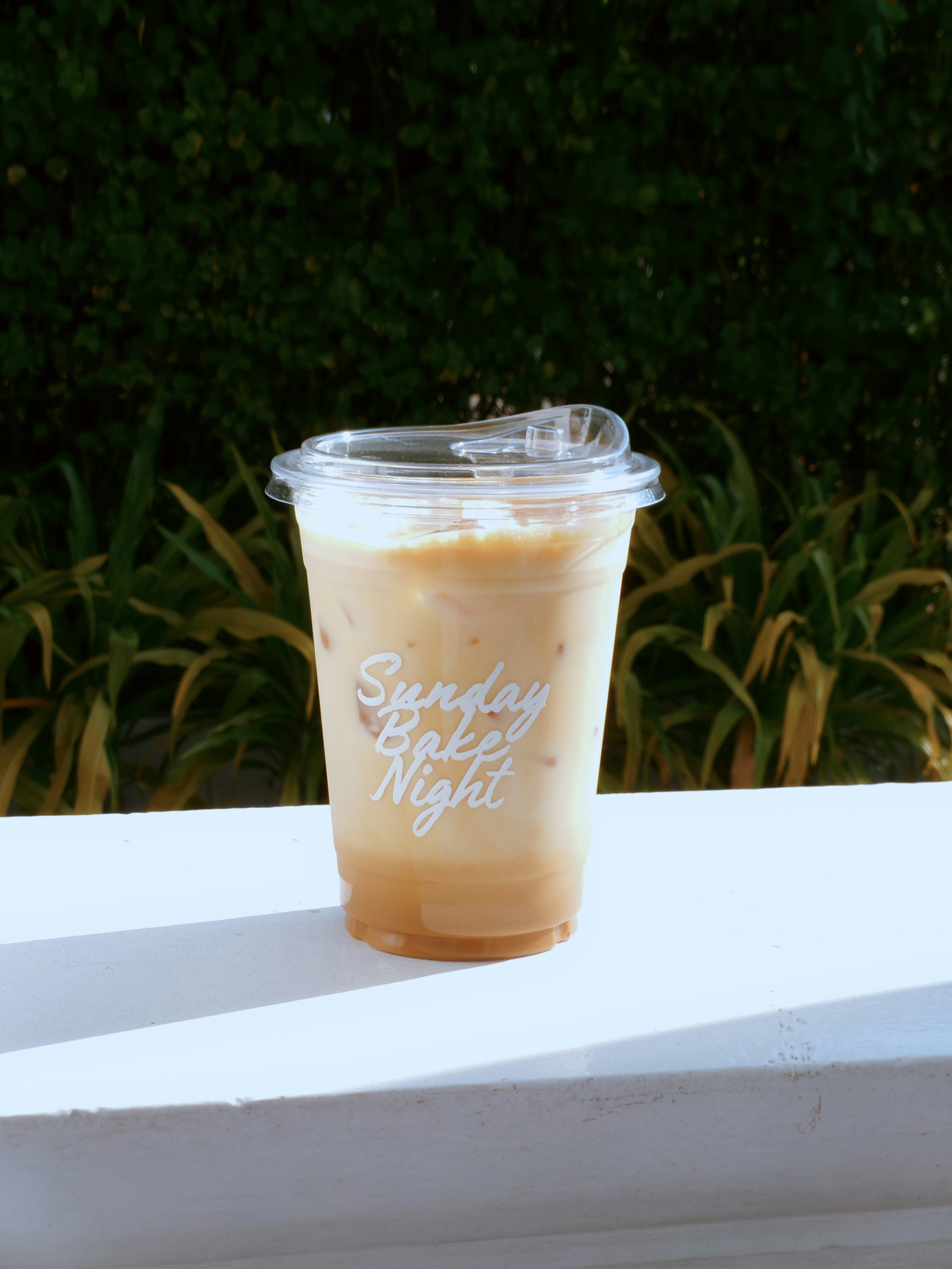 Sunlit iced latte on a white ledge with a garden backdrop