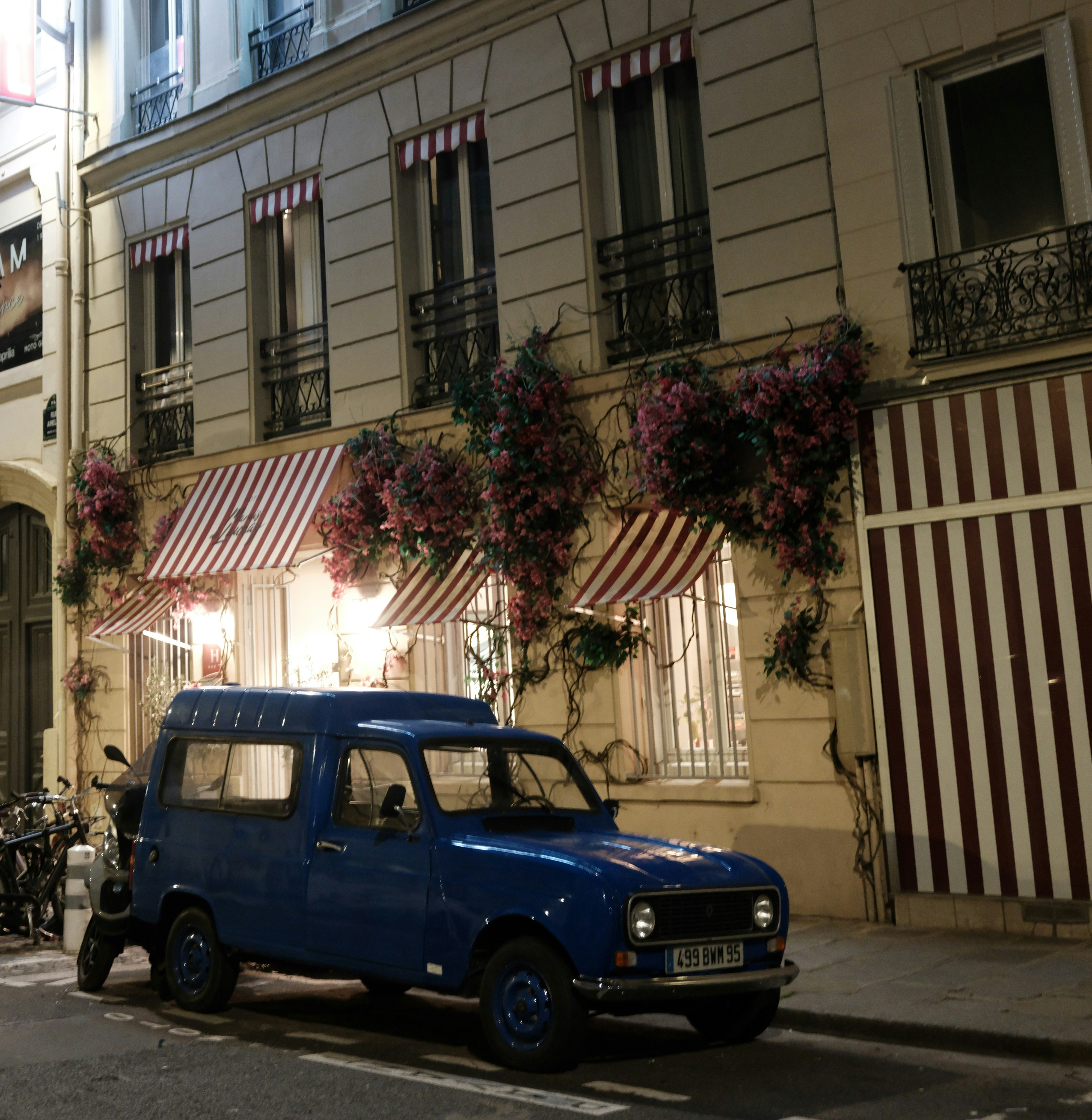 Blue van under striped canopies on a Parisian street at dusk