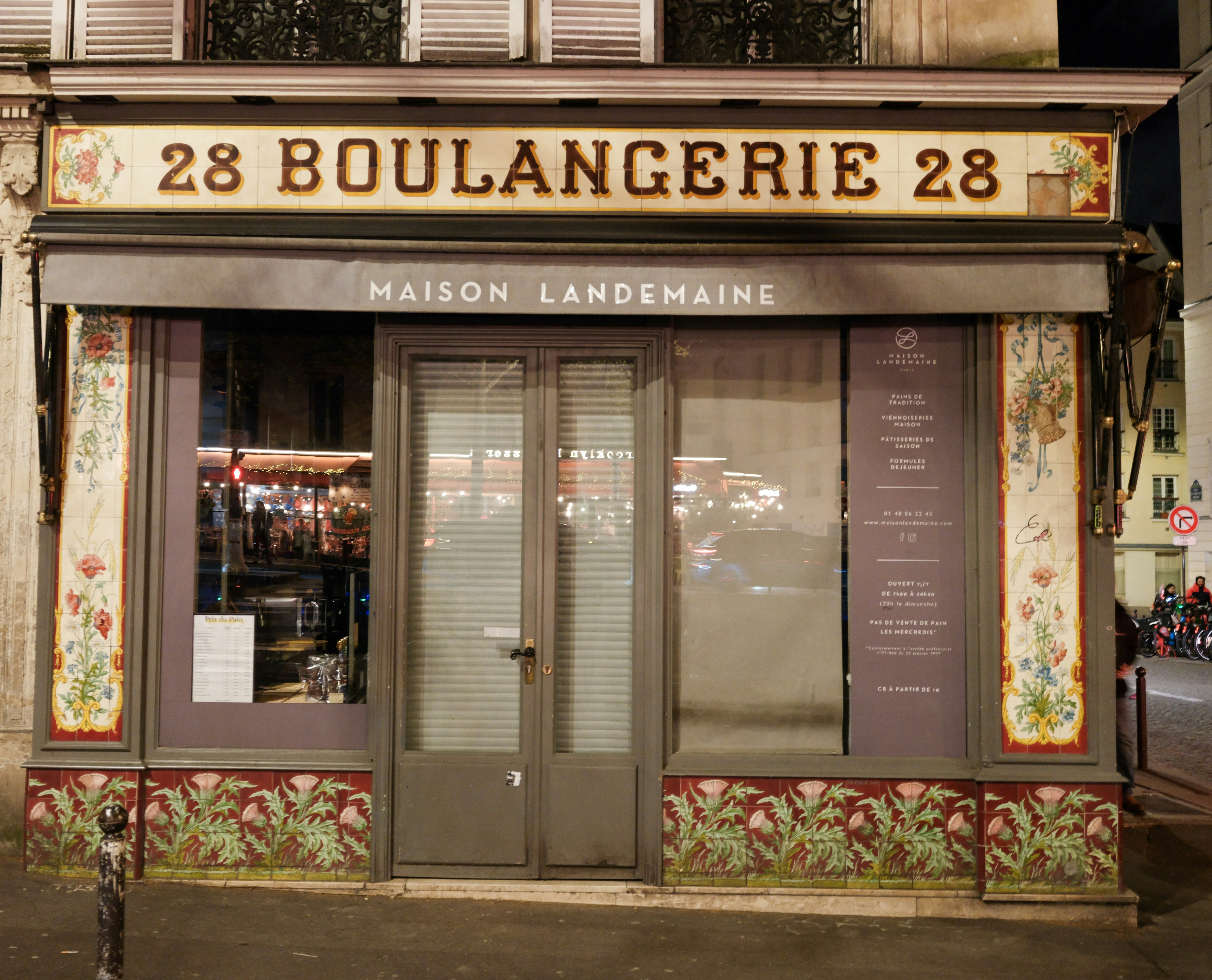 Charming Parisian storefront with ornate signage, glass doors, and a muted awning that reads Maison Landemaine, captured at dusk with warm interior lights.
